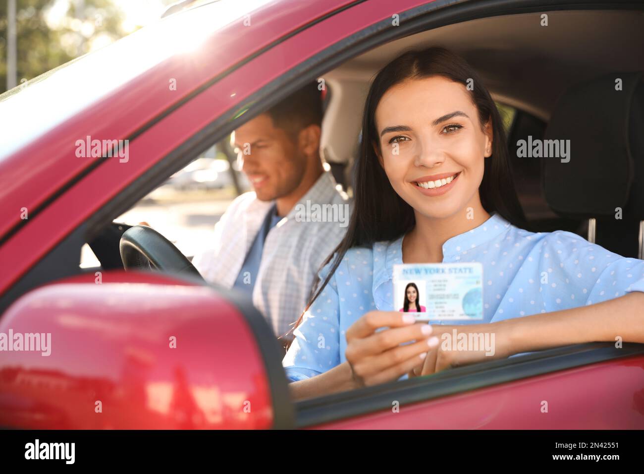 Young woman holding license while sitting in car with instructor ...