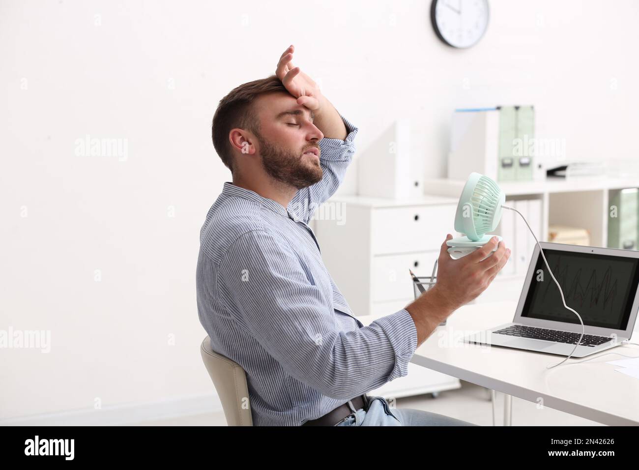 Man enjoying air flow from fan at workplace Stock Photo - Alamy