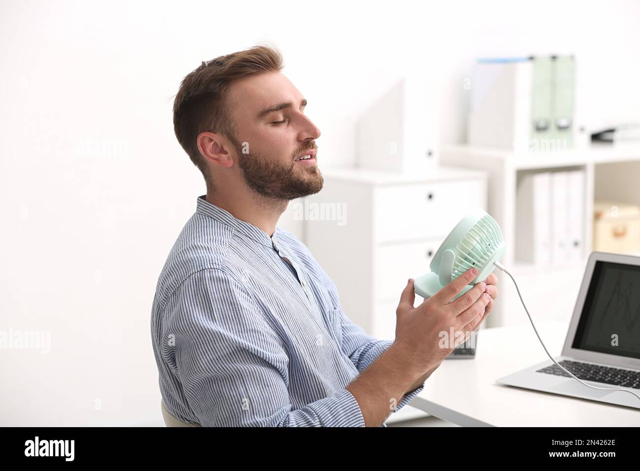 Man enjoying air flow from fan at workplace Stock Photo - Alamy
