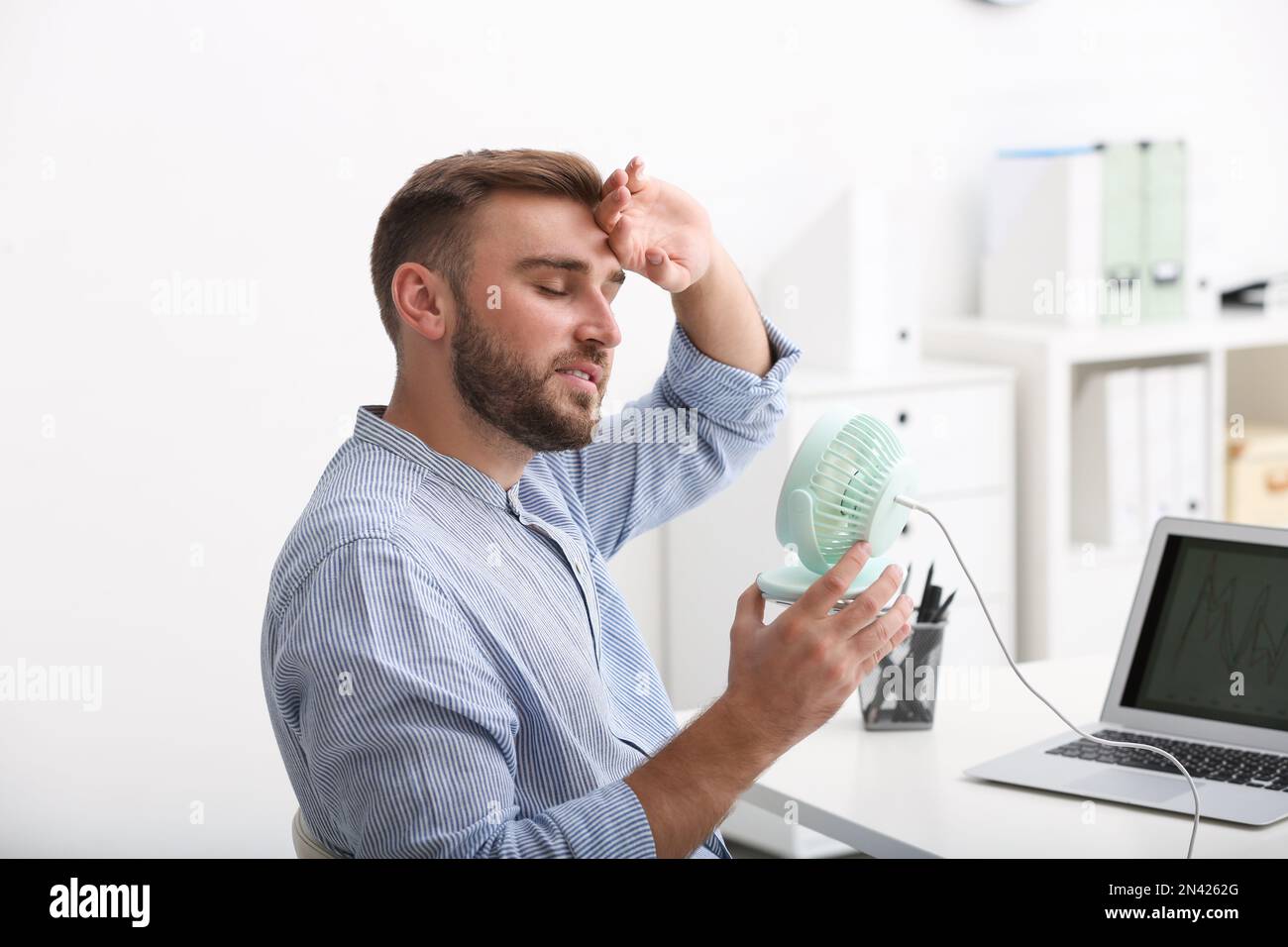 Man enjoying air flow from fan at workplace Stock Photo - Alamy
