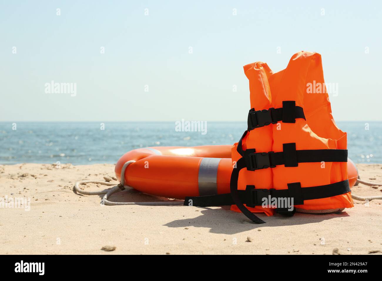 Orange life jacket and buoy on sandy beach near sea. Emergency rescue ...