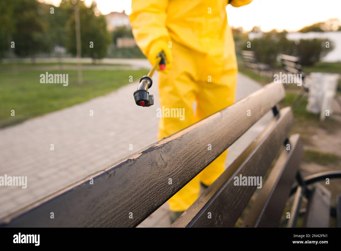 Person in hazmat suit disinfecting bench in park with sprayer, closeup ...