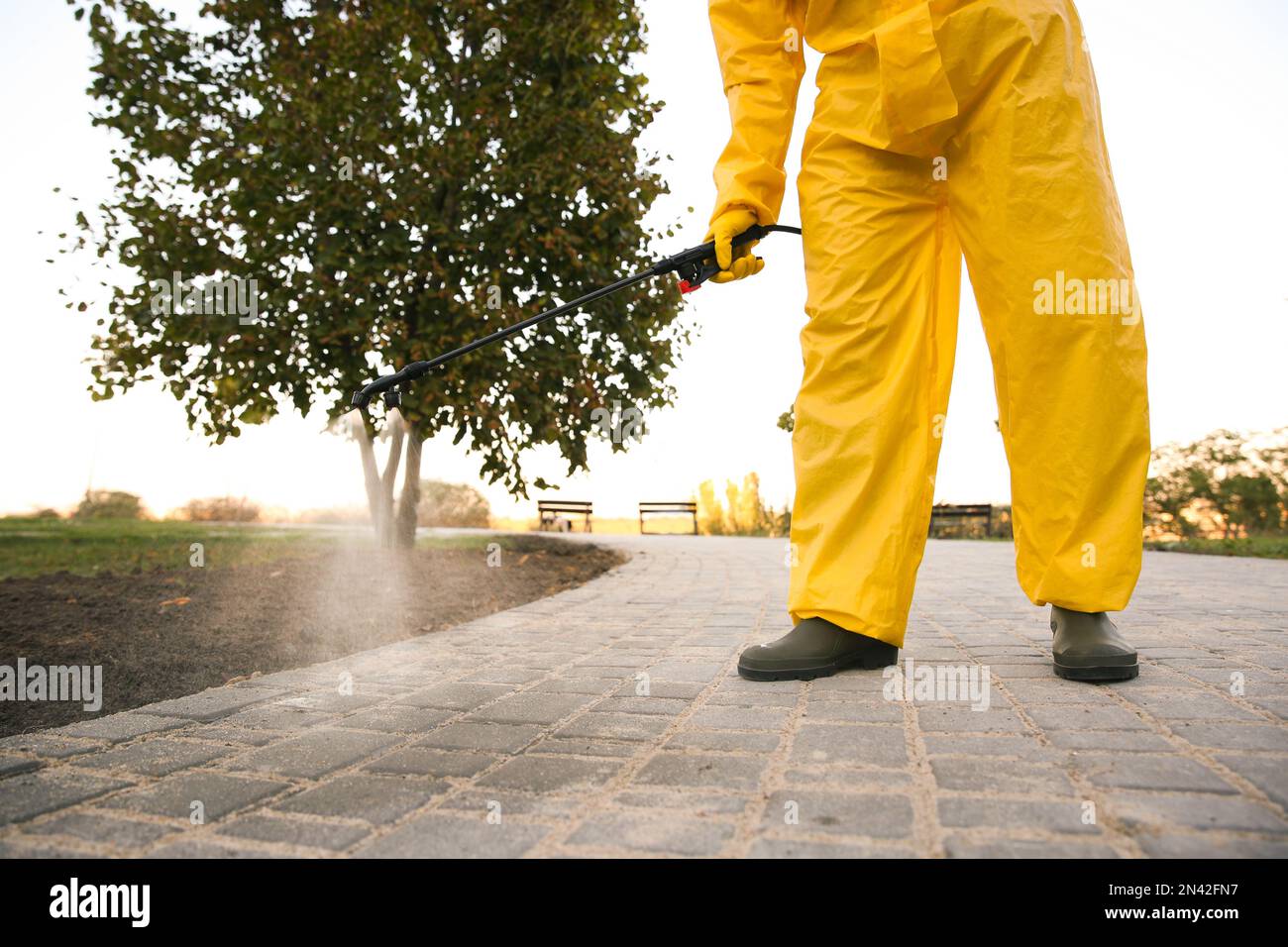 Person in hazmat suit disinfecting pavement in park with sprayer ...