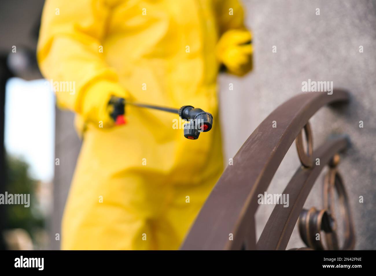 Person in hazmat suit disinfecting railing, focus on sprayer. Surface ...