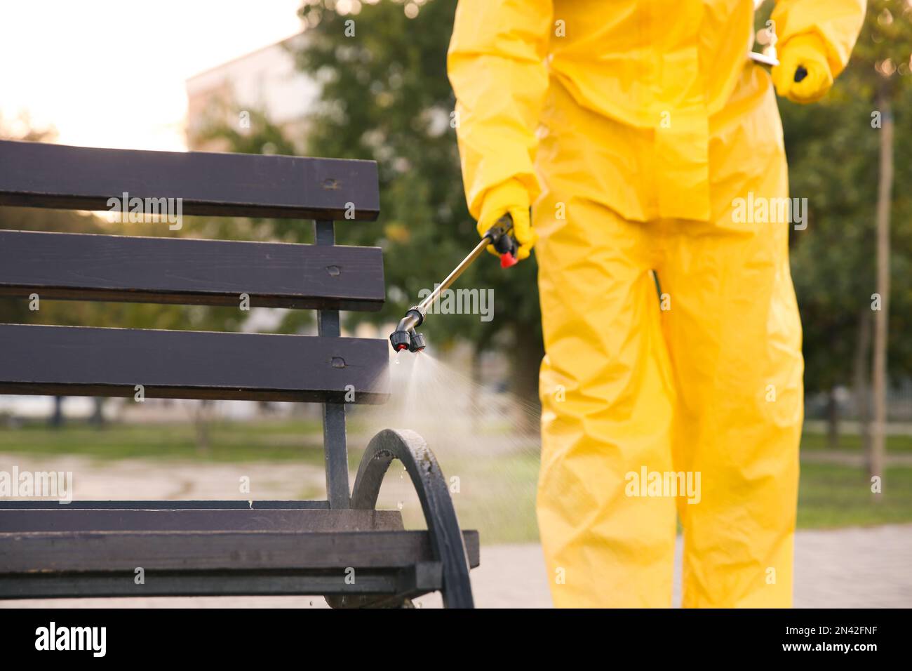 Person in hazmat suit disinfecting bench in park with sprayer, closeup ...