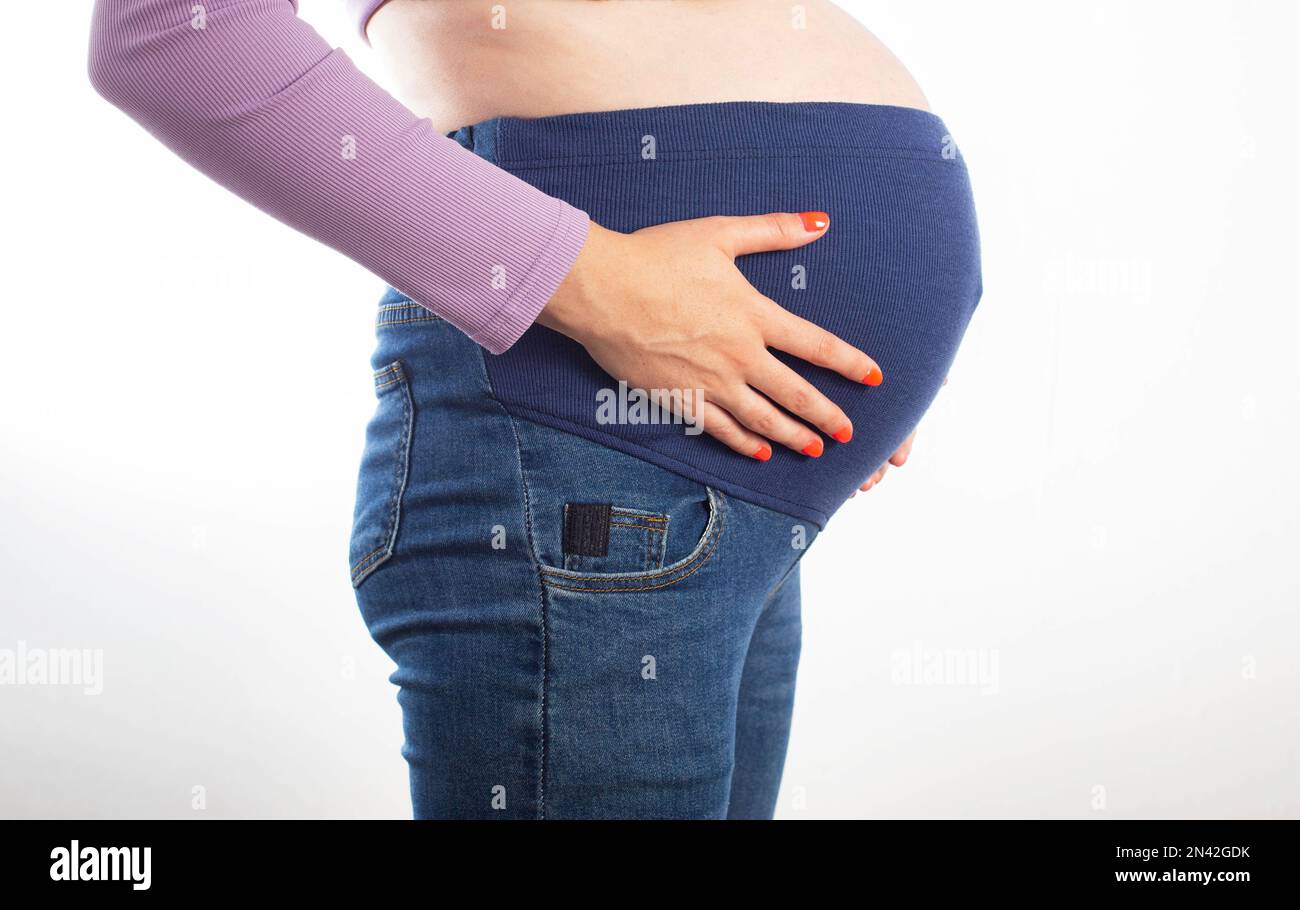 Pregnant girl with a big belly in jeans on a white background. The ...