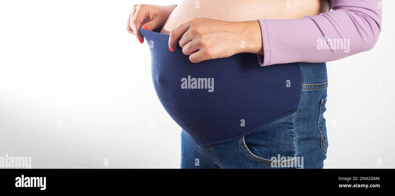 Pregnant girl with a big belly in jeans on a white background. The ...