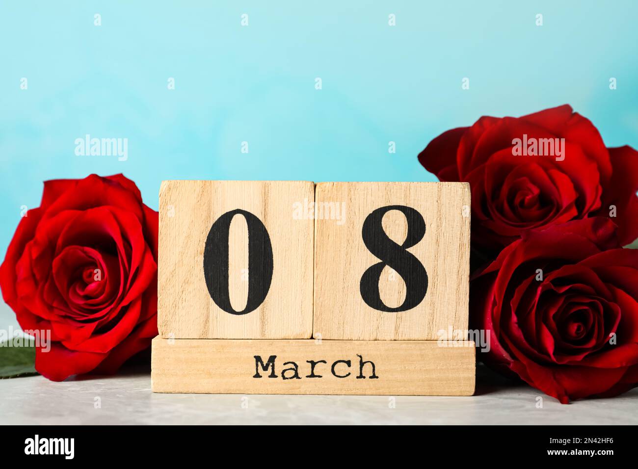 Wooden block calendar with date 8th of March and roses on table against ...