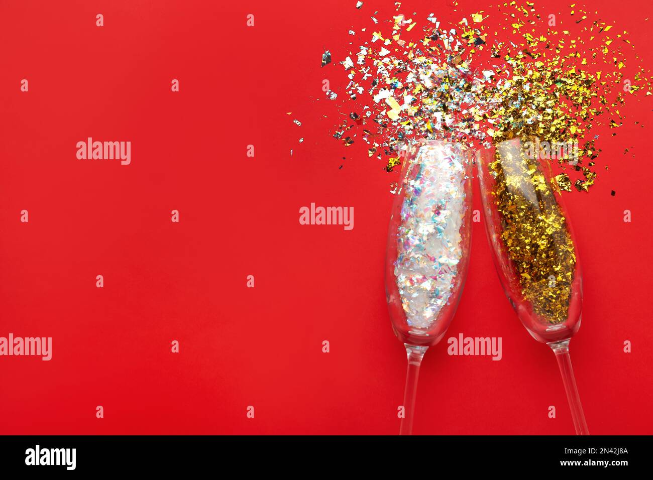 Shiny confetti spilled out of champagne glasses on red background, flat ...