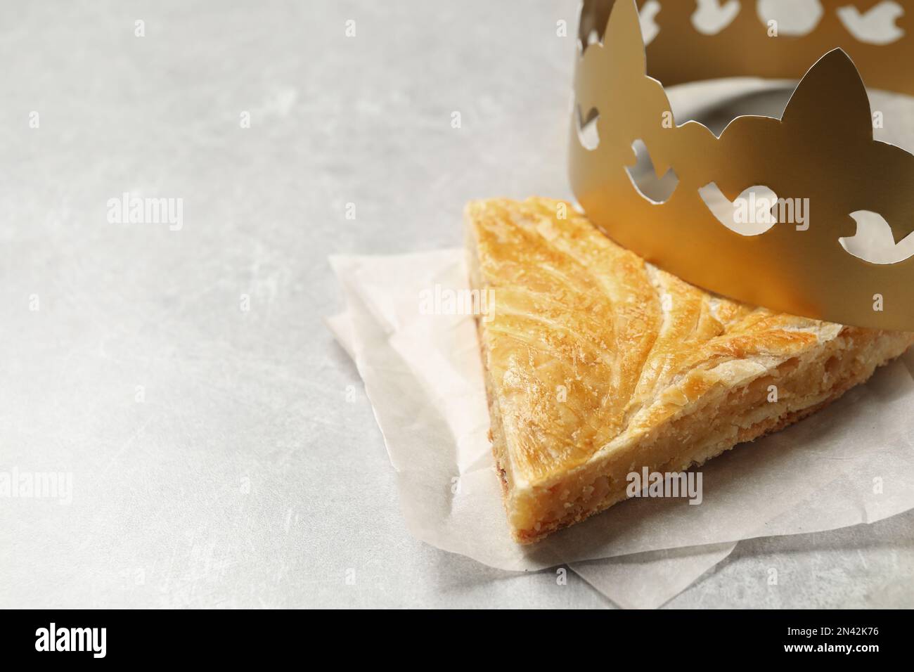 Slice of traditional galette des Rois with paper crown on light grey ...