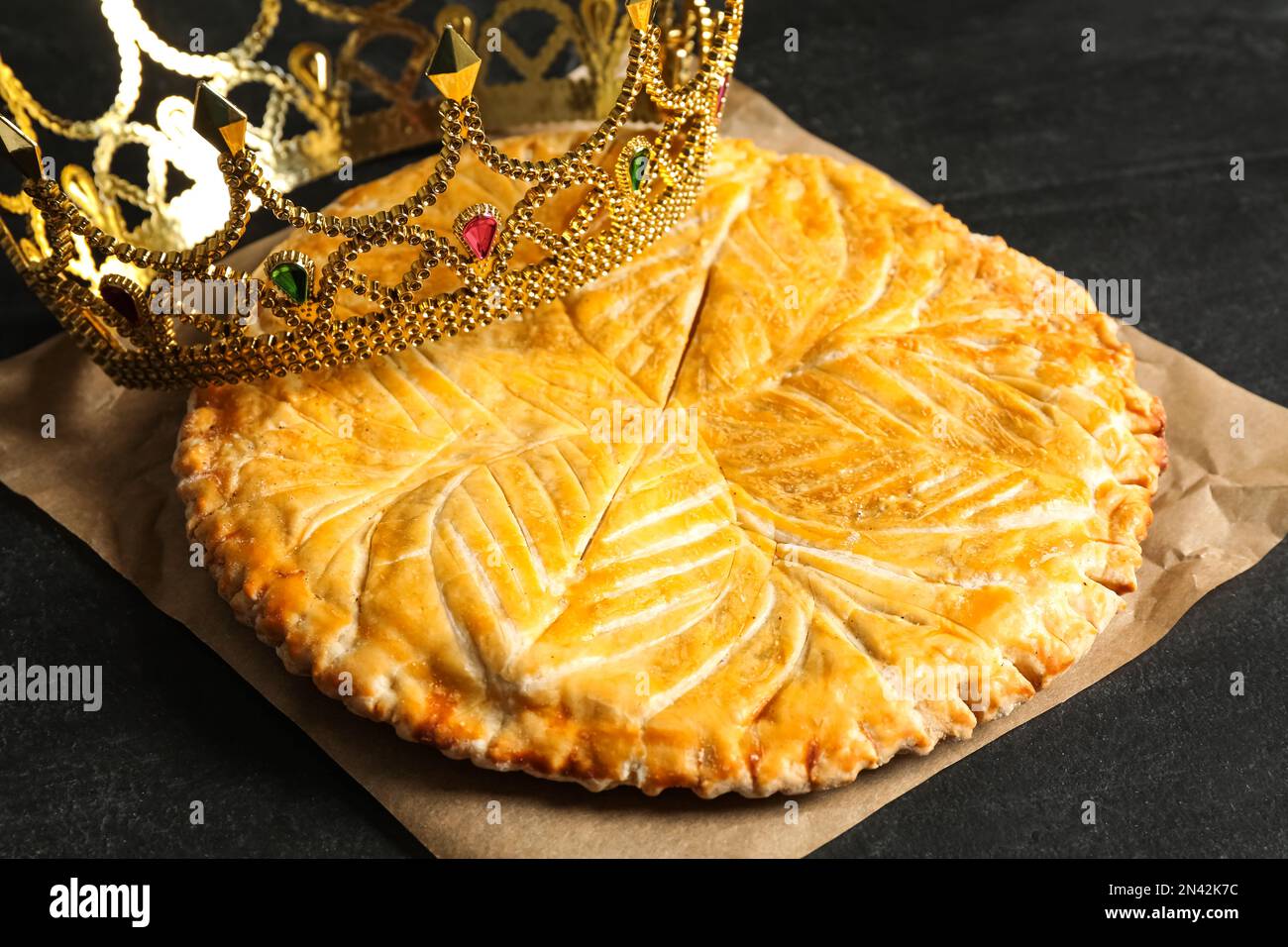 Traditional galette des Rois with decorative crown on black table ...