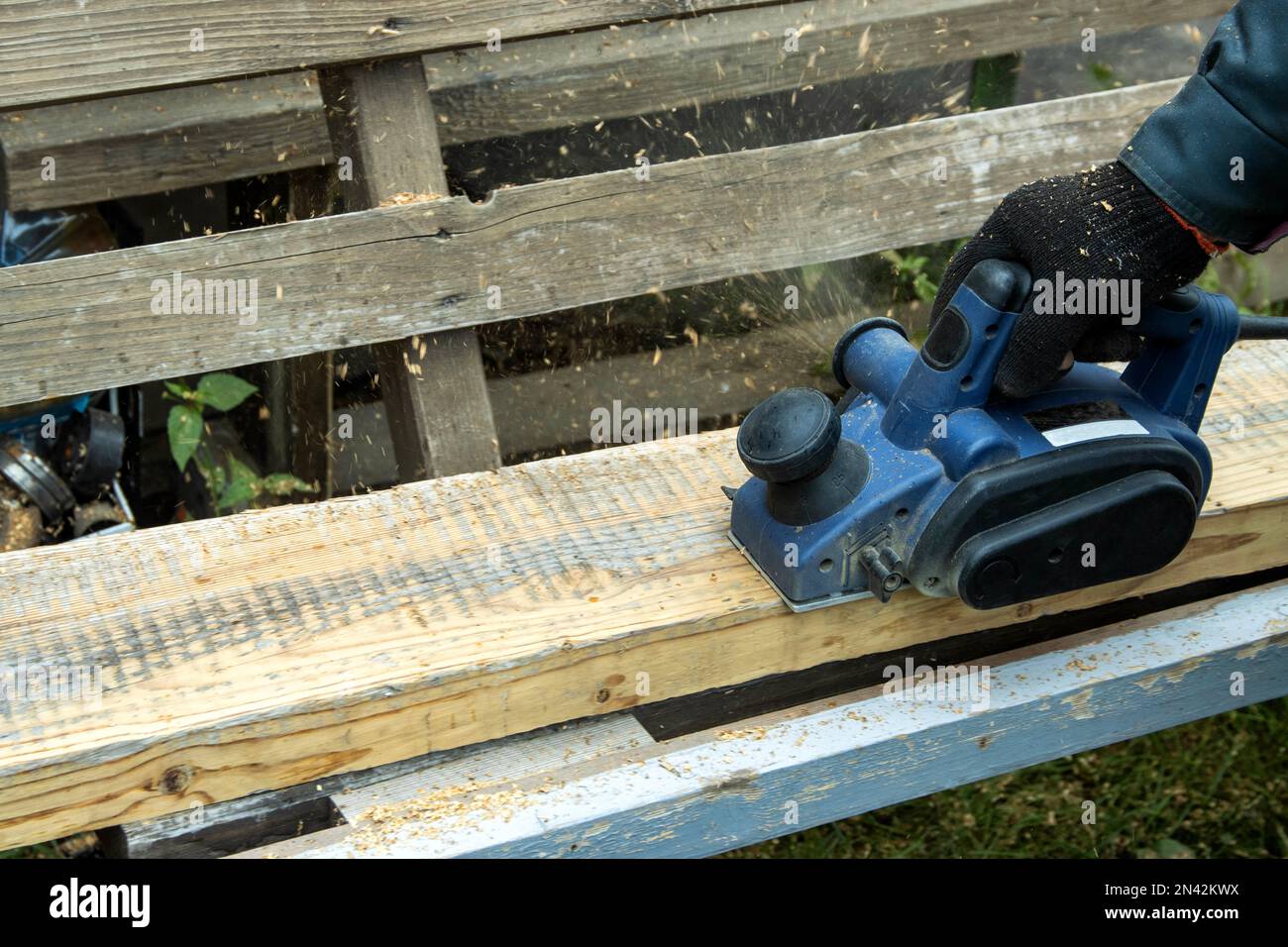 A male carpenter plans boards with an electric planer to make a bench ...
