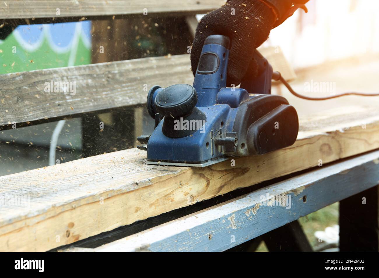 A male carpenter plans boards with an electric planer to make a bench ...