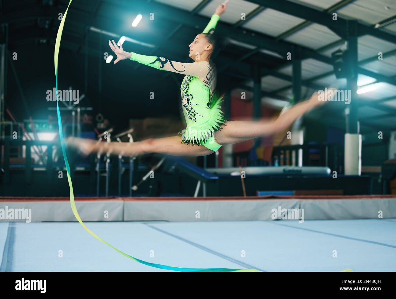 Gymnastics, woman and jump with ribbon and motion blur, sport in gym ...