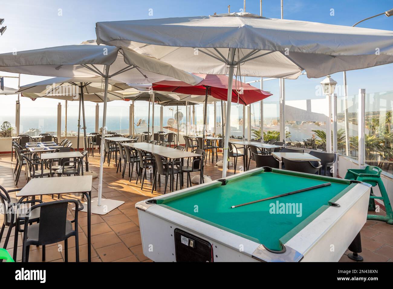 A pool table with a cue and no balls under the umbrella of outdoor cafe ...