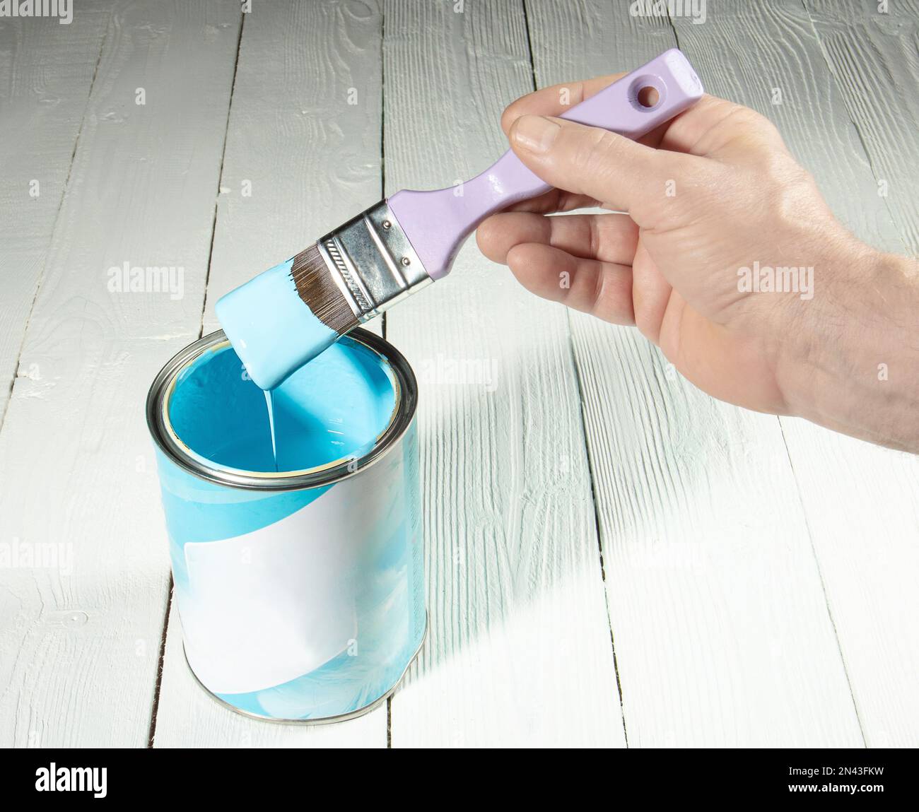 The hand holds a brush with a light blue paint flowing from it in a jar ...