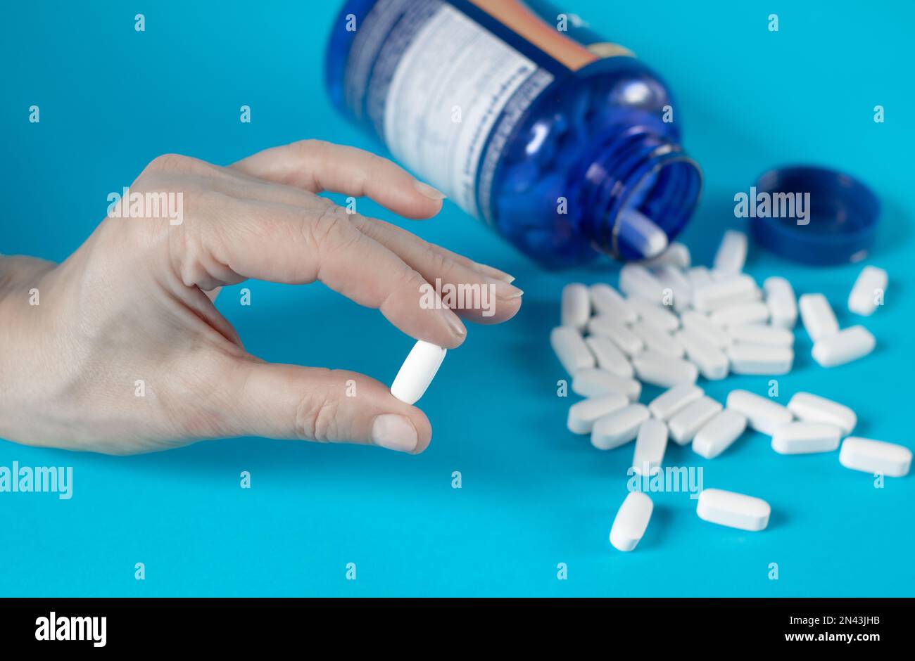 Female fingers hold a large white pill with bioadditives on a blue ...
