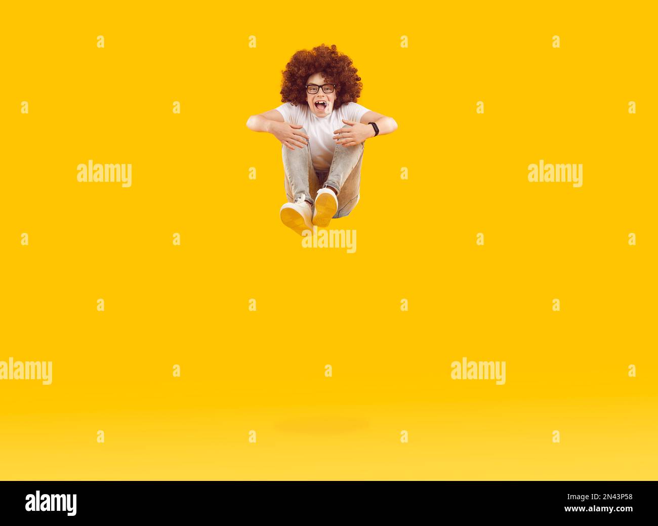 Happy funny boy in curly wig jumping up, screaming and flying in air on ...