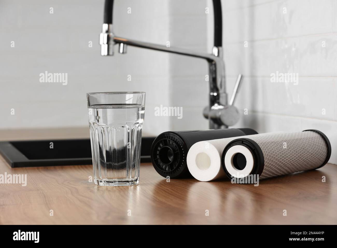 A glass of clean fresh water and set of filter cartridges on wooden ...