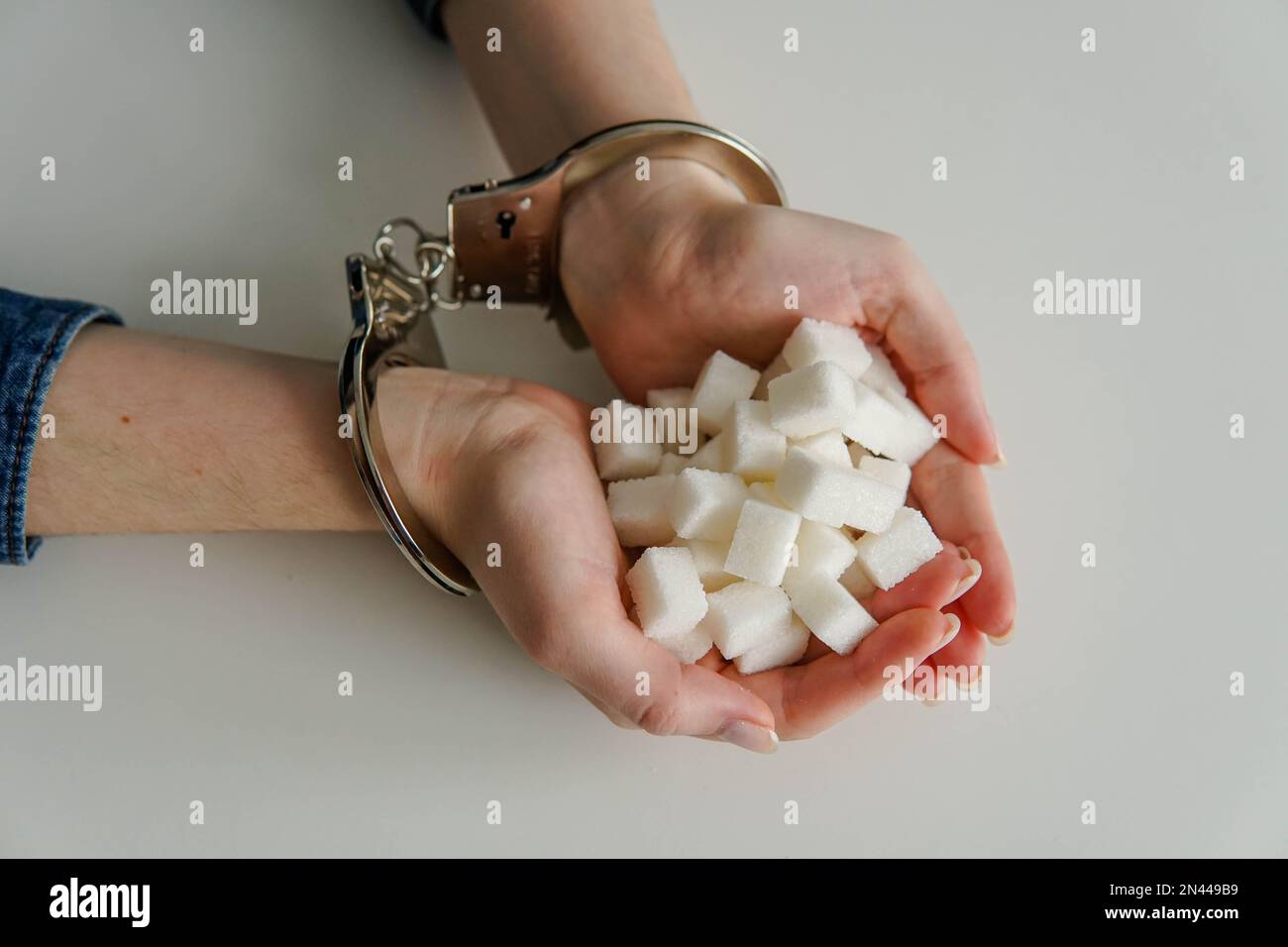 Young woman in handcuffs with white sugar cubes on the table. Sugar ...