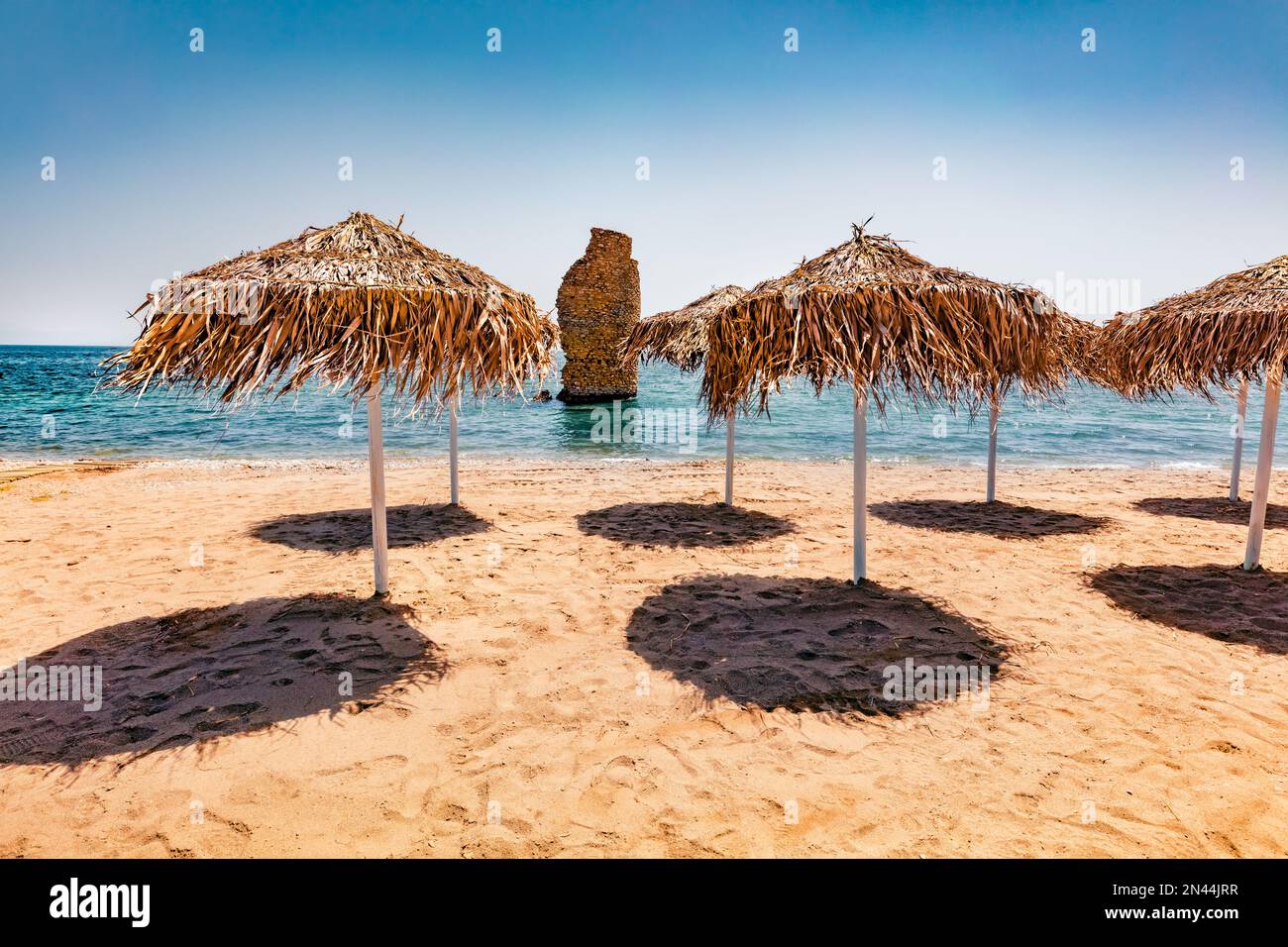 Empty Mylos Beach with sun umbrellas and ruins of old Roman tower on ...