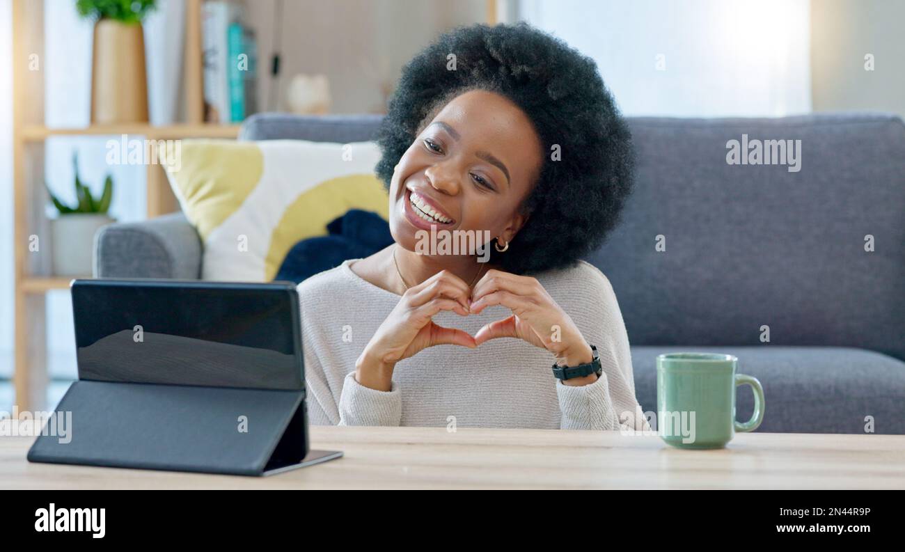 Woman making a heart gesture and talking on video call with a tablet at ...