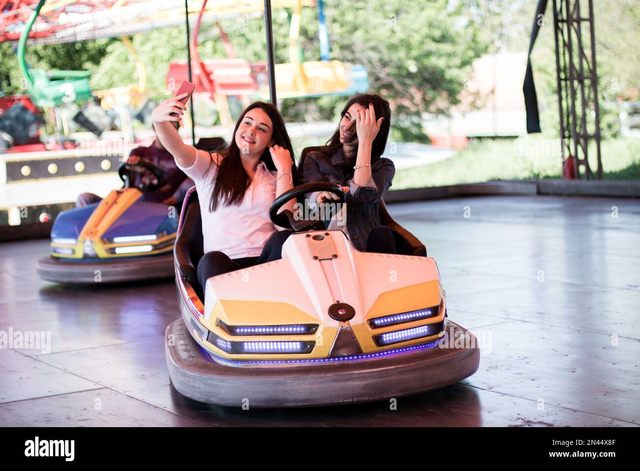 Two young women on a fun bumper car ride at the amusement park, taking ...