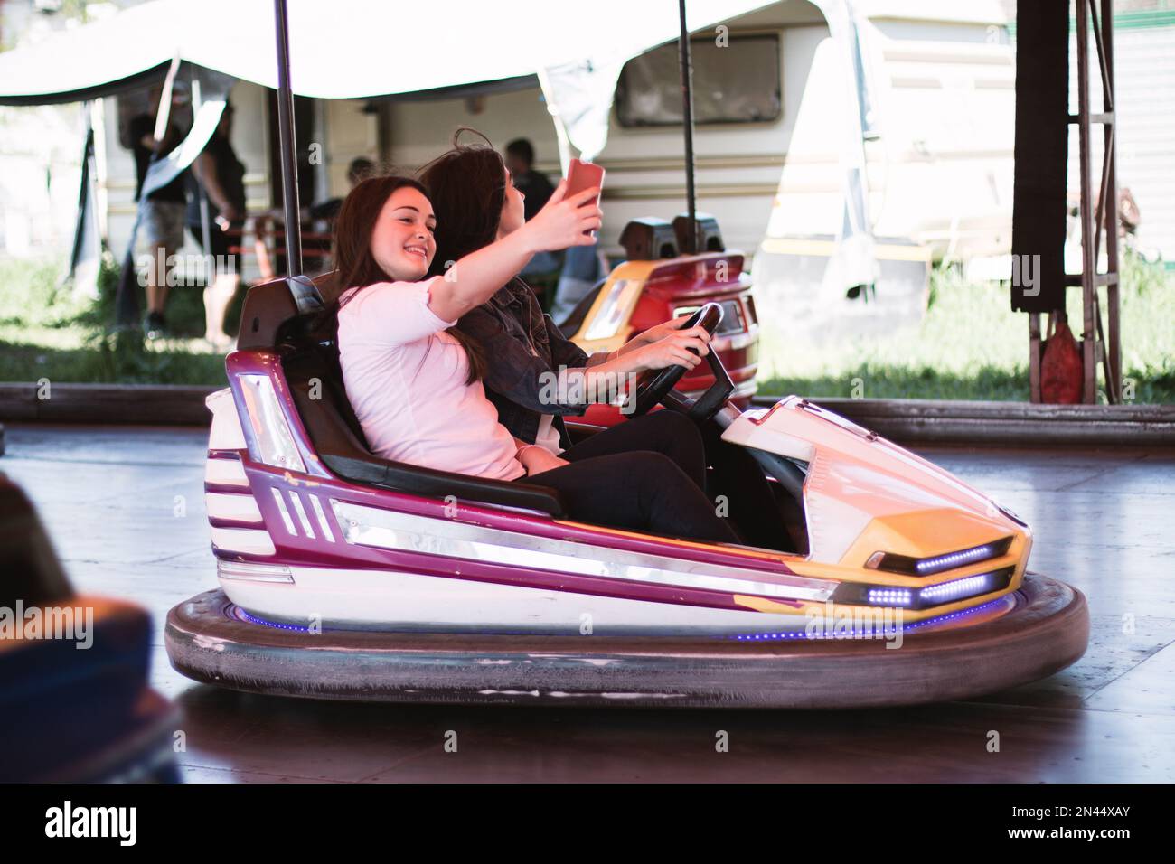 Two young women on a fun bumper car ride at the amusement park, taking ...