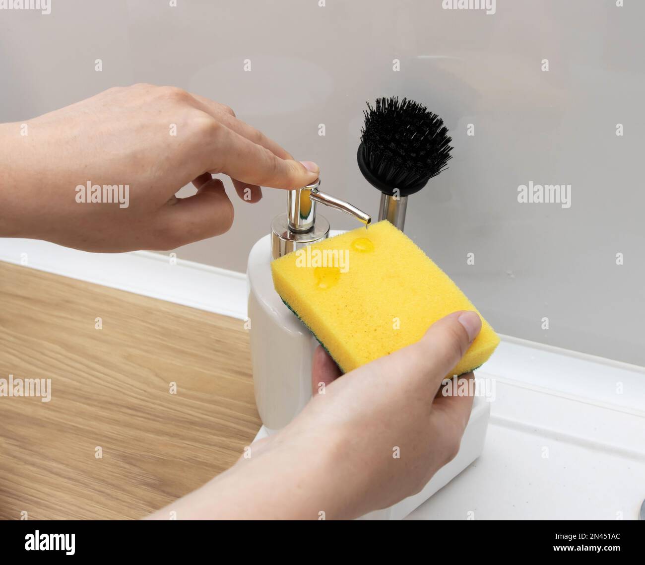 A girl applies an anti-grease detergent to a dishwashing sponge. White ...