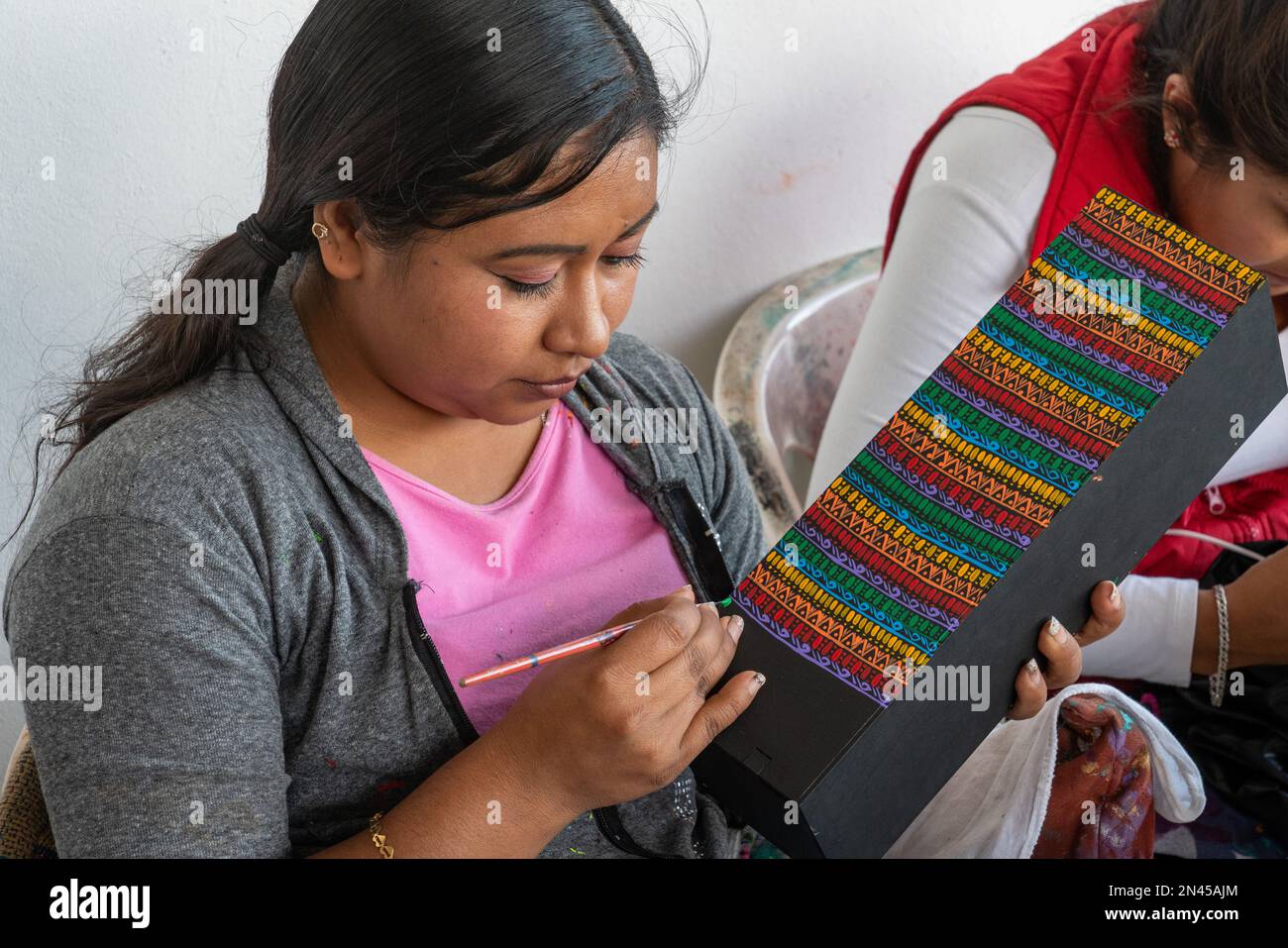 Artisans paint Zapotec designs on boxes for bottles of mescal in a shop ...