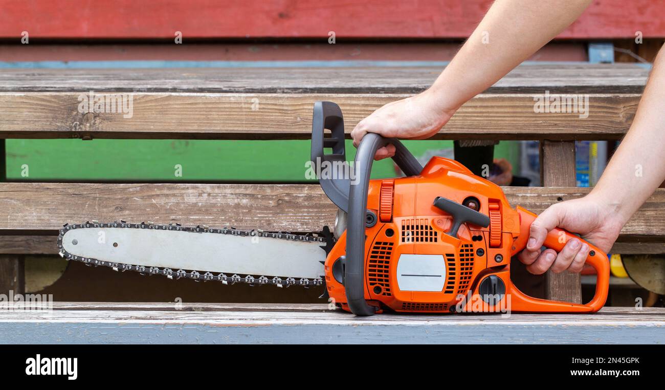 Hands of a worker with a chainsaw on a wood background. Concept worker ...