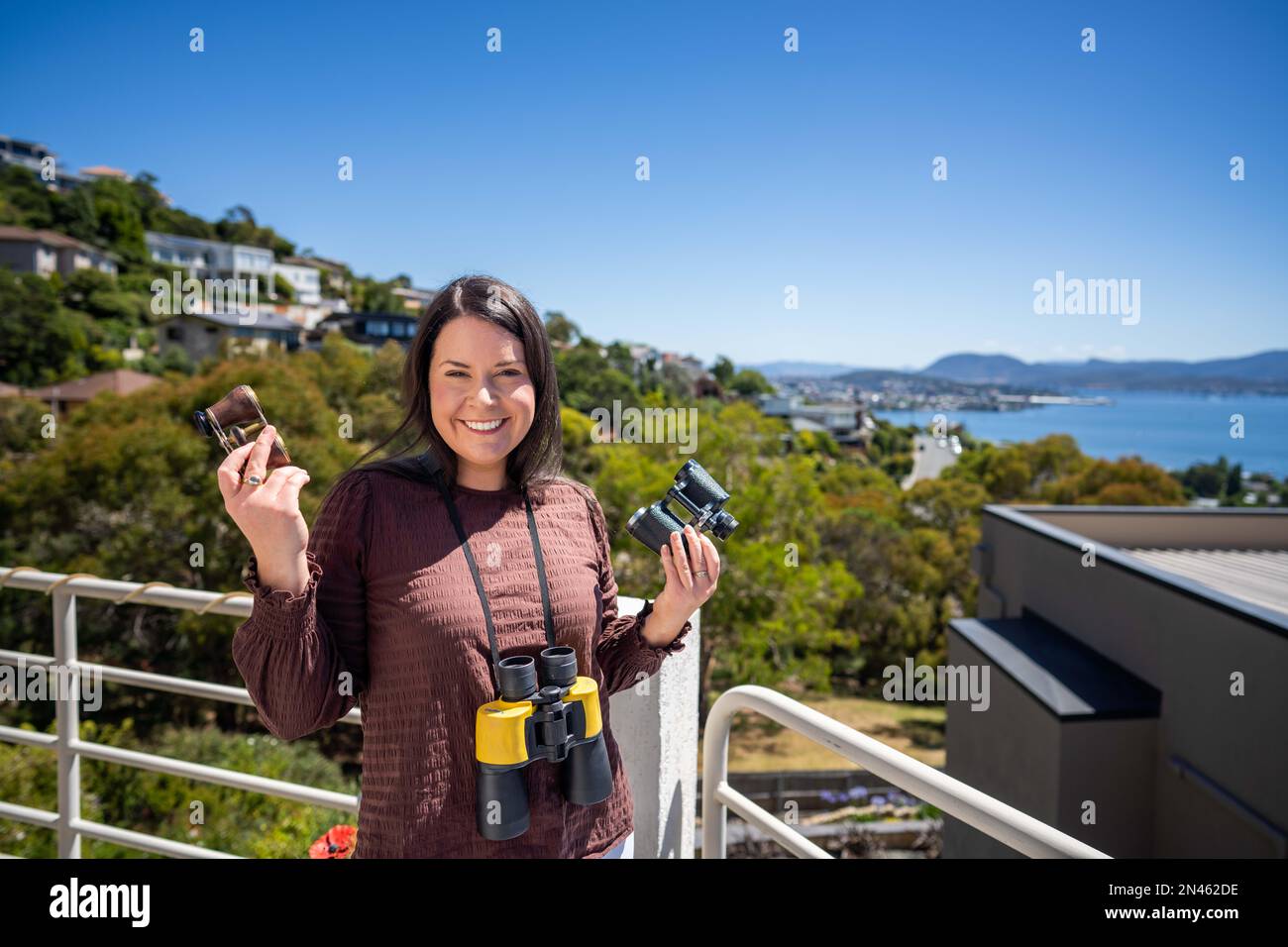 Girl using binoculars on a balcony in a city next to the sea, seaside ...