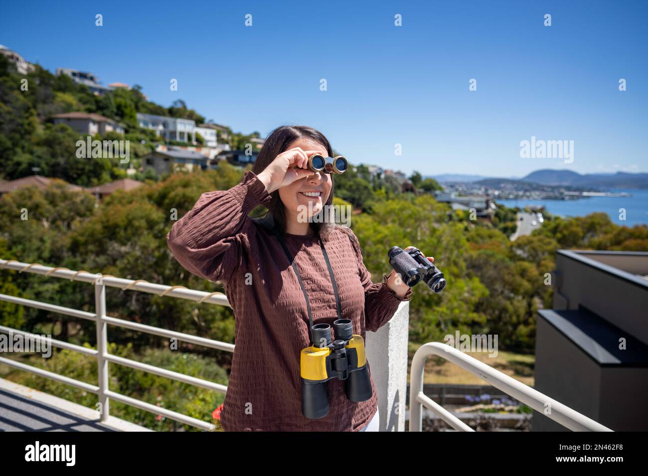 Girl using binoculars on a balcony in a city next to the sea, seaside ...