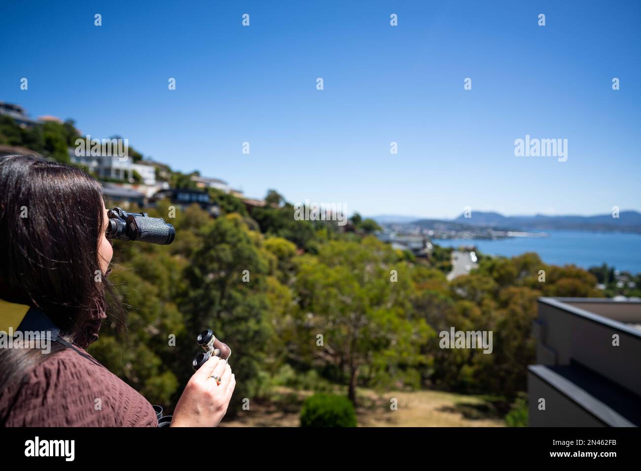 Girl using binoculars on a balcony in a city next to the sea, seaside ...