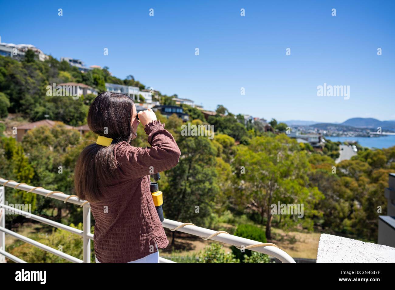 Girl using binoculars on a balcony in a city next to the sea, seaside ...
