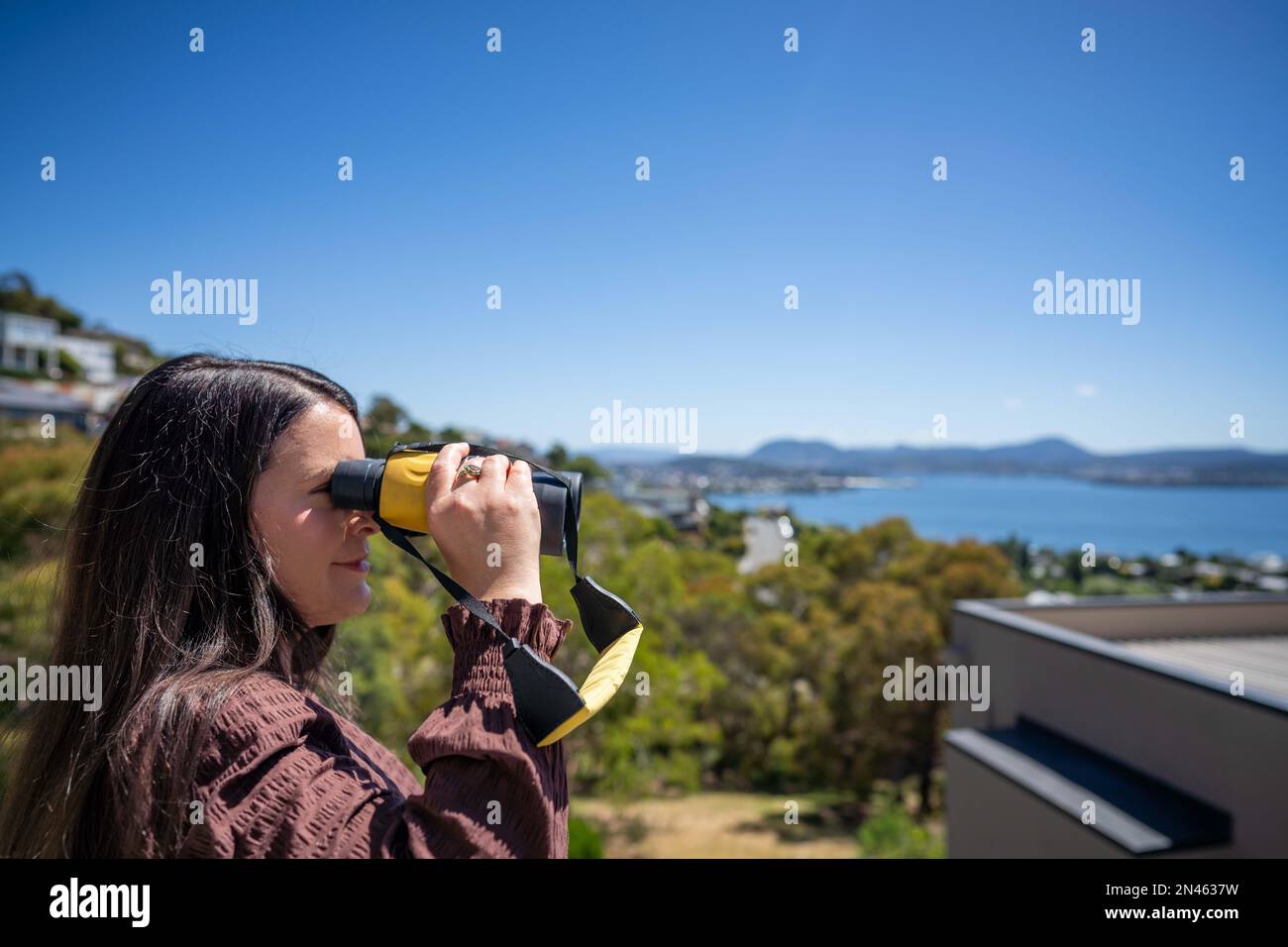 Girl using binoculars on a balcony in a city next to the sea, seaside ...
