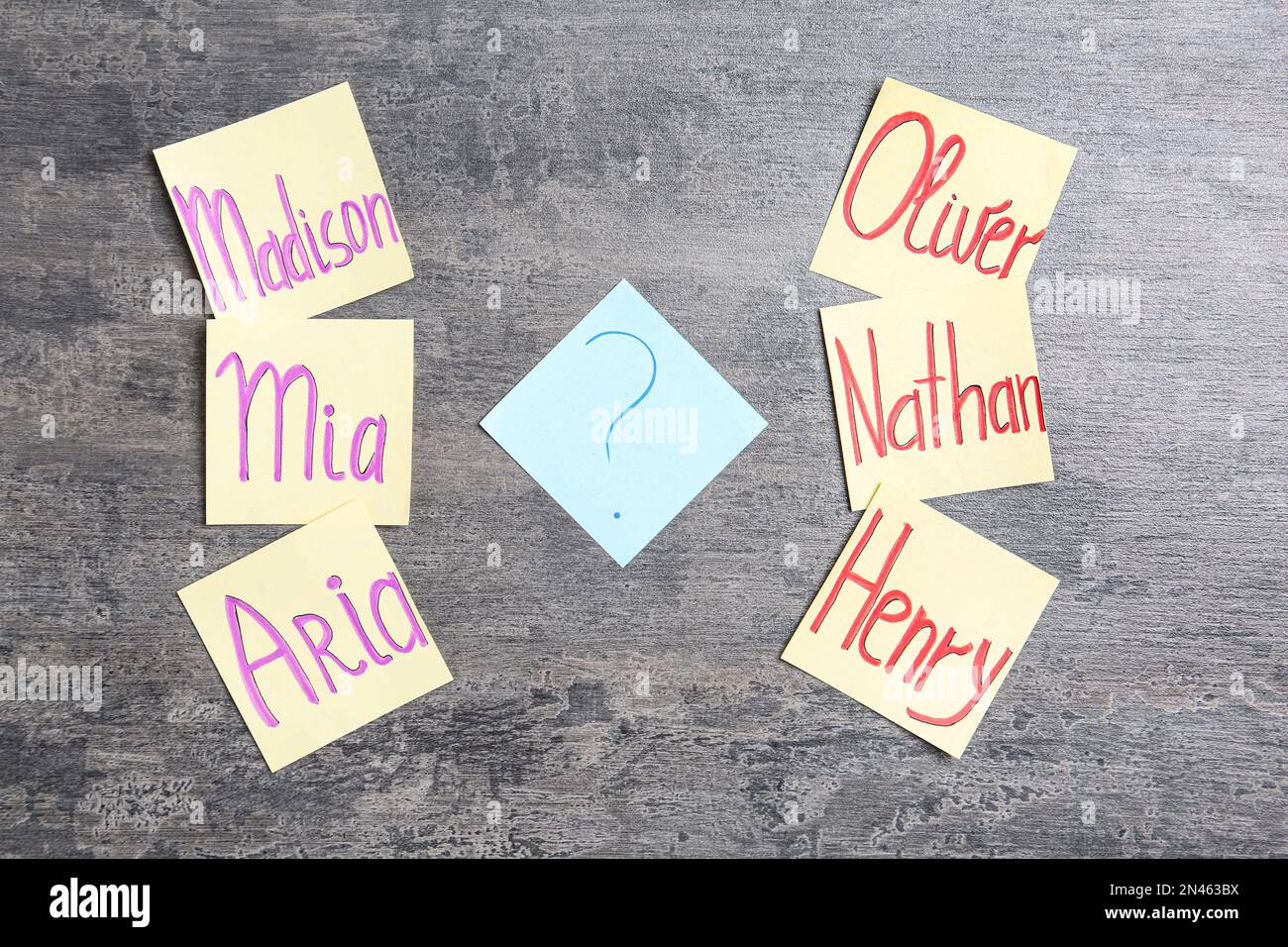 Paper notes with different baby names and question mark on grey table ...