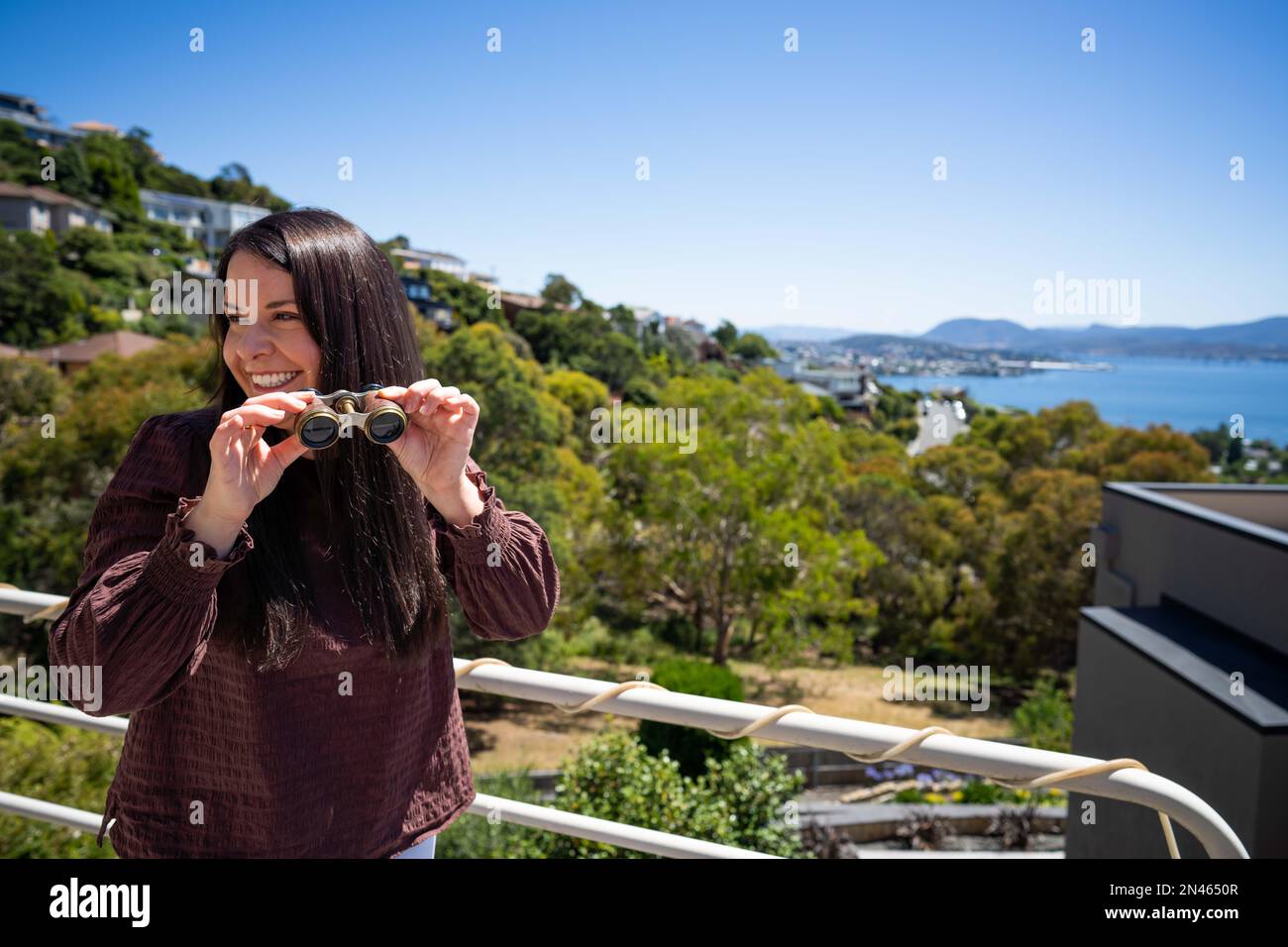 Girl using binoculars on a balcony in a city next to the sea, seaside ...