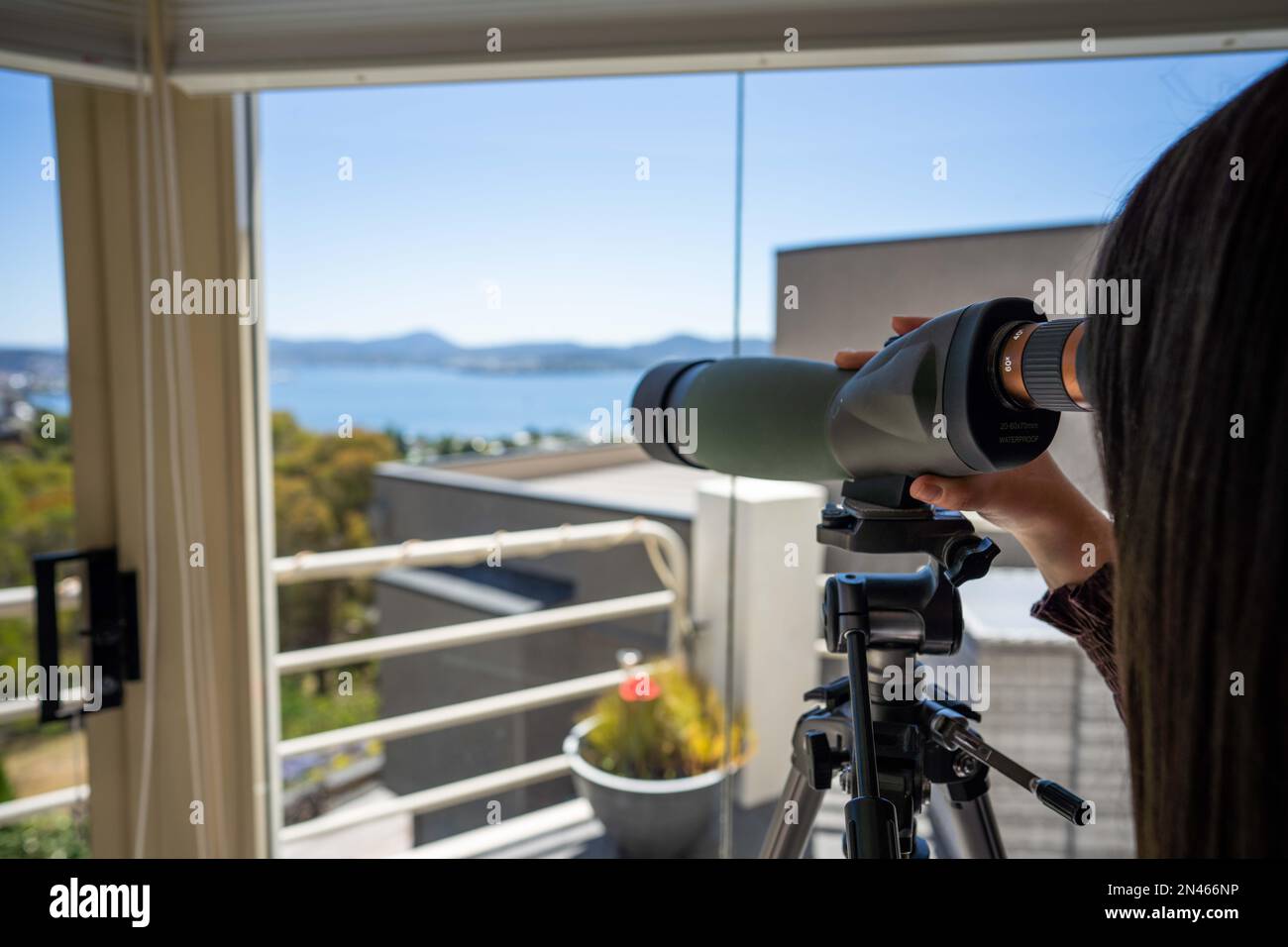 Girl using binoculars on a balcony in a city next to the sea, seaside ...