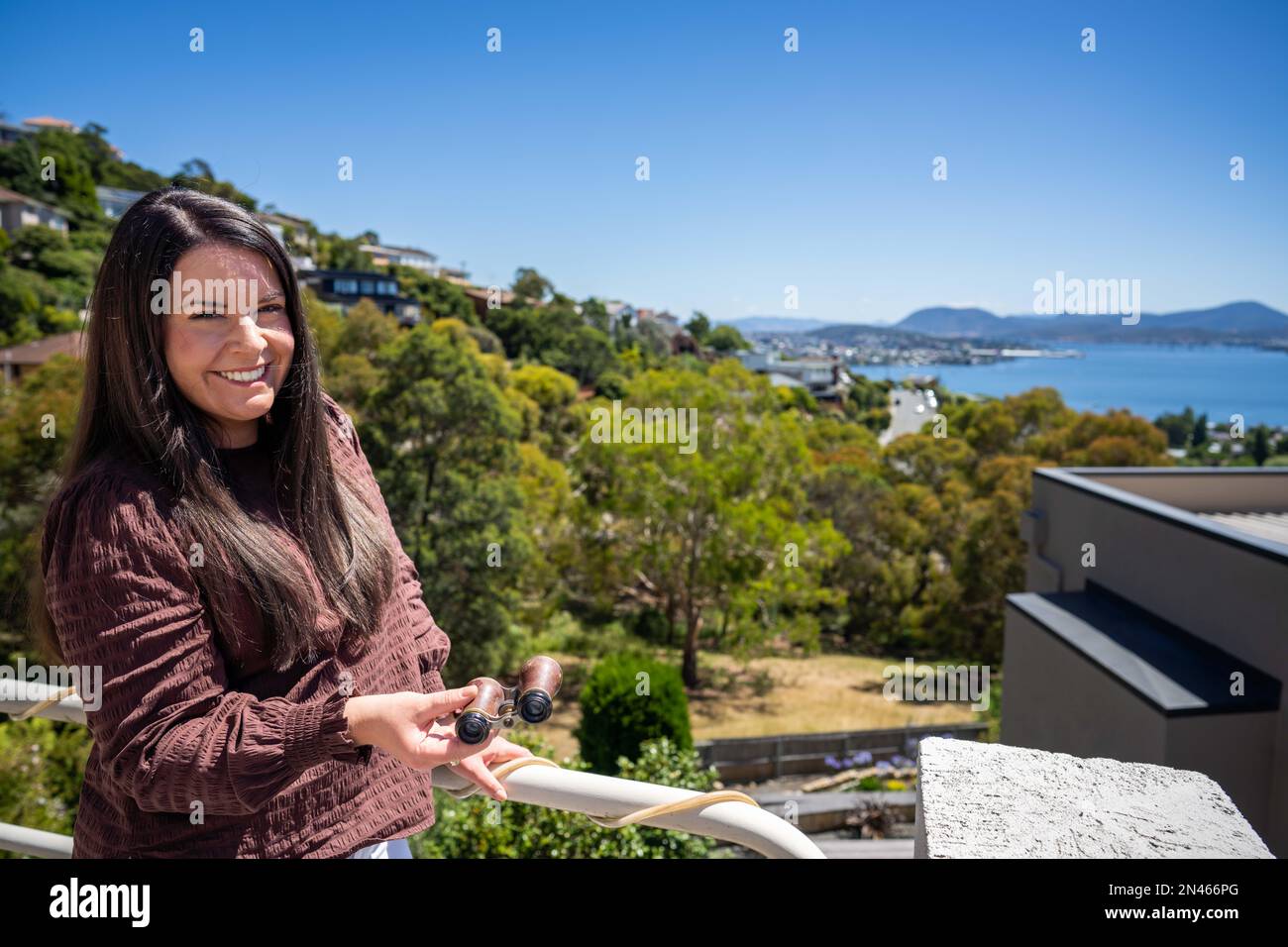 Girl using binoculars on a balcony in a city next to the sea, seaside ...