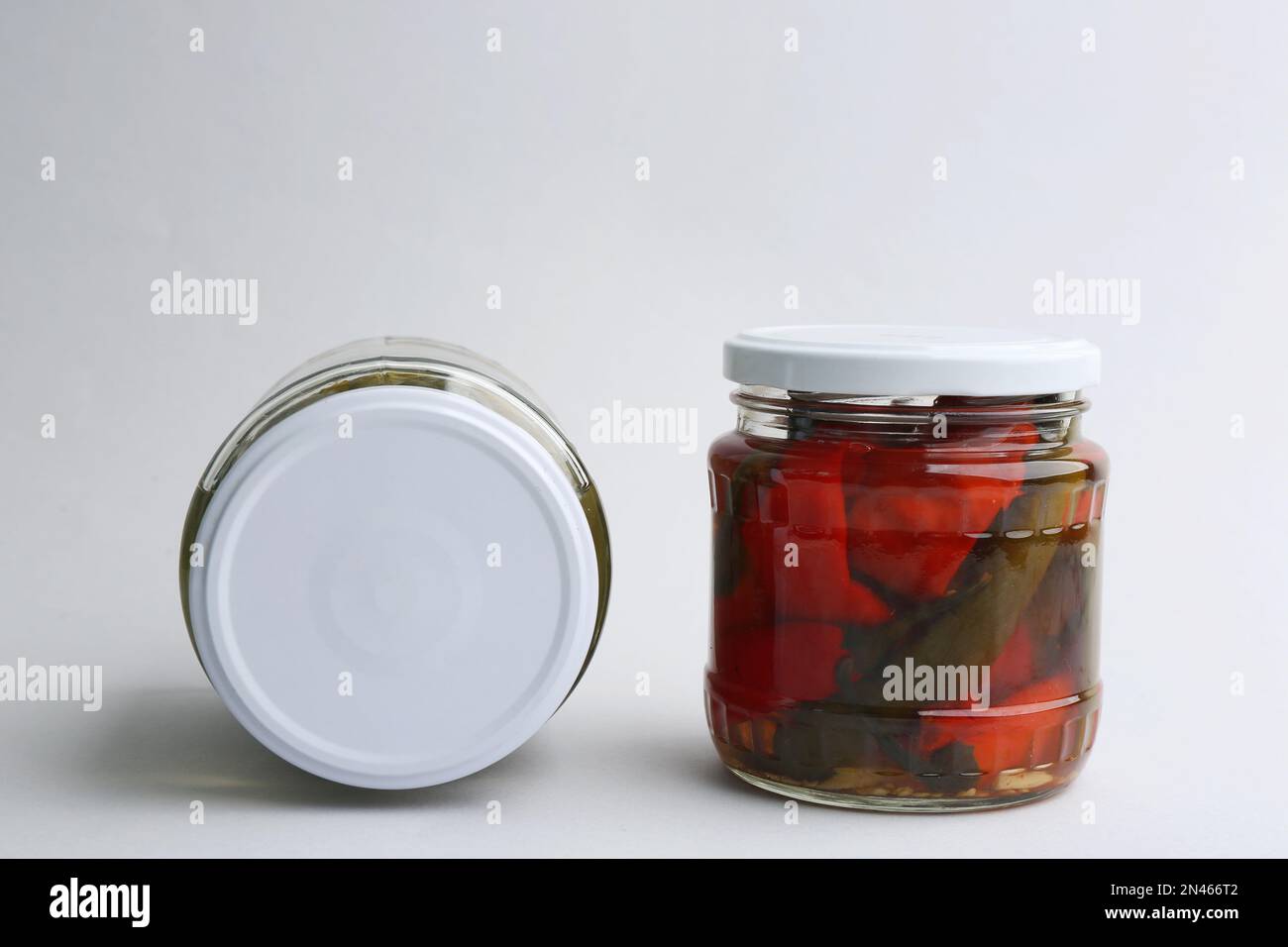 Glass jars with pickled bell peppers and cucumbers on white background ...