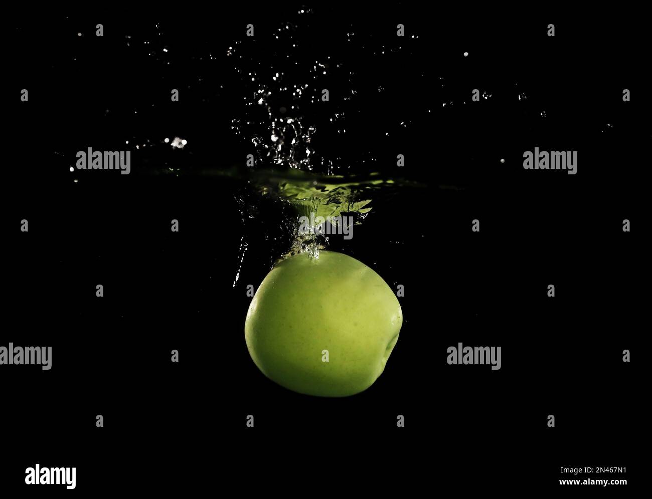 Green apple falling down into clear water against black background ...