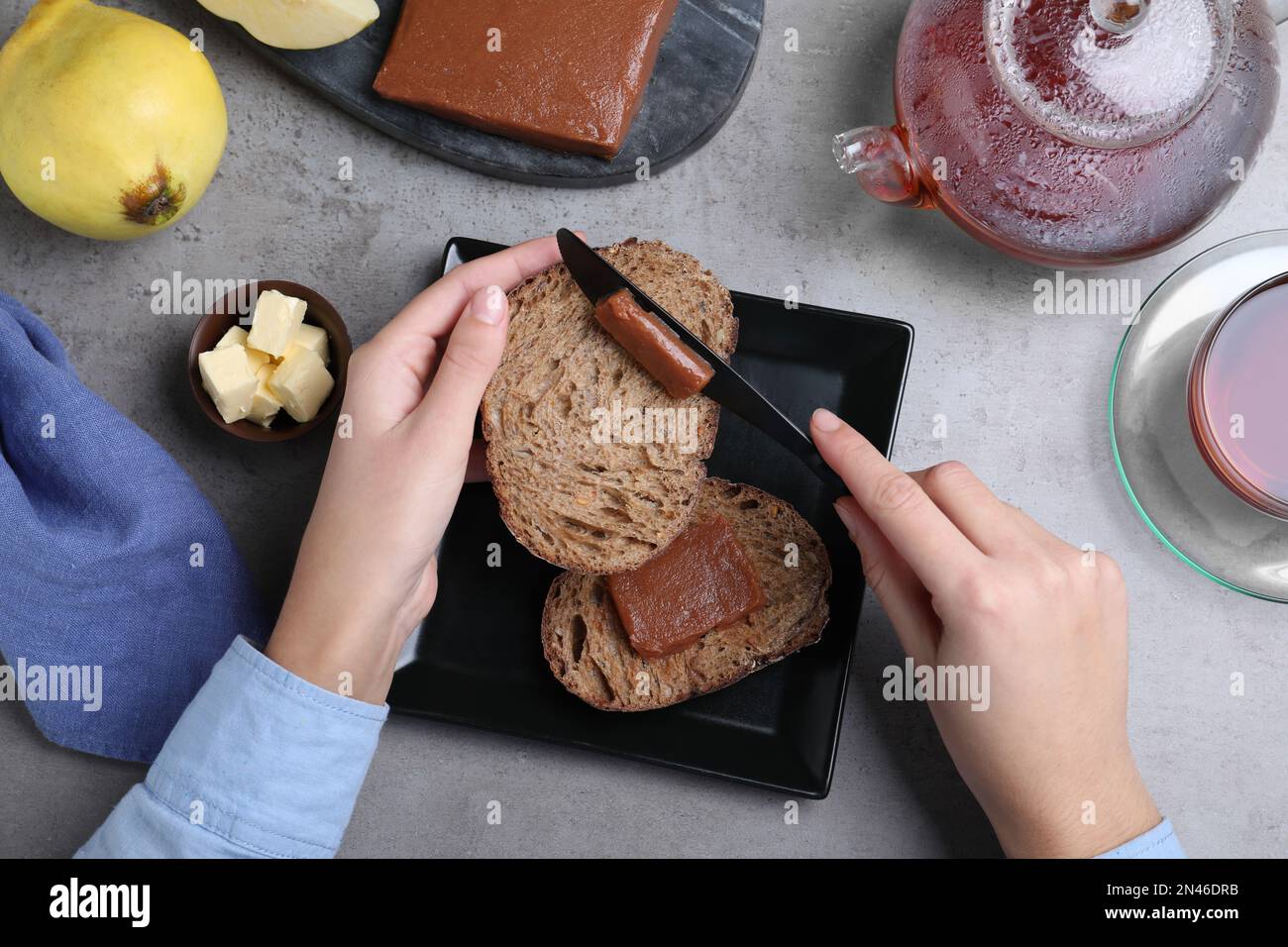 Woman spreading delicious quince paste on toast bread at grey table ...