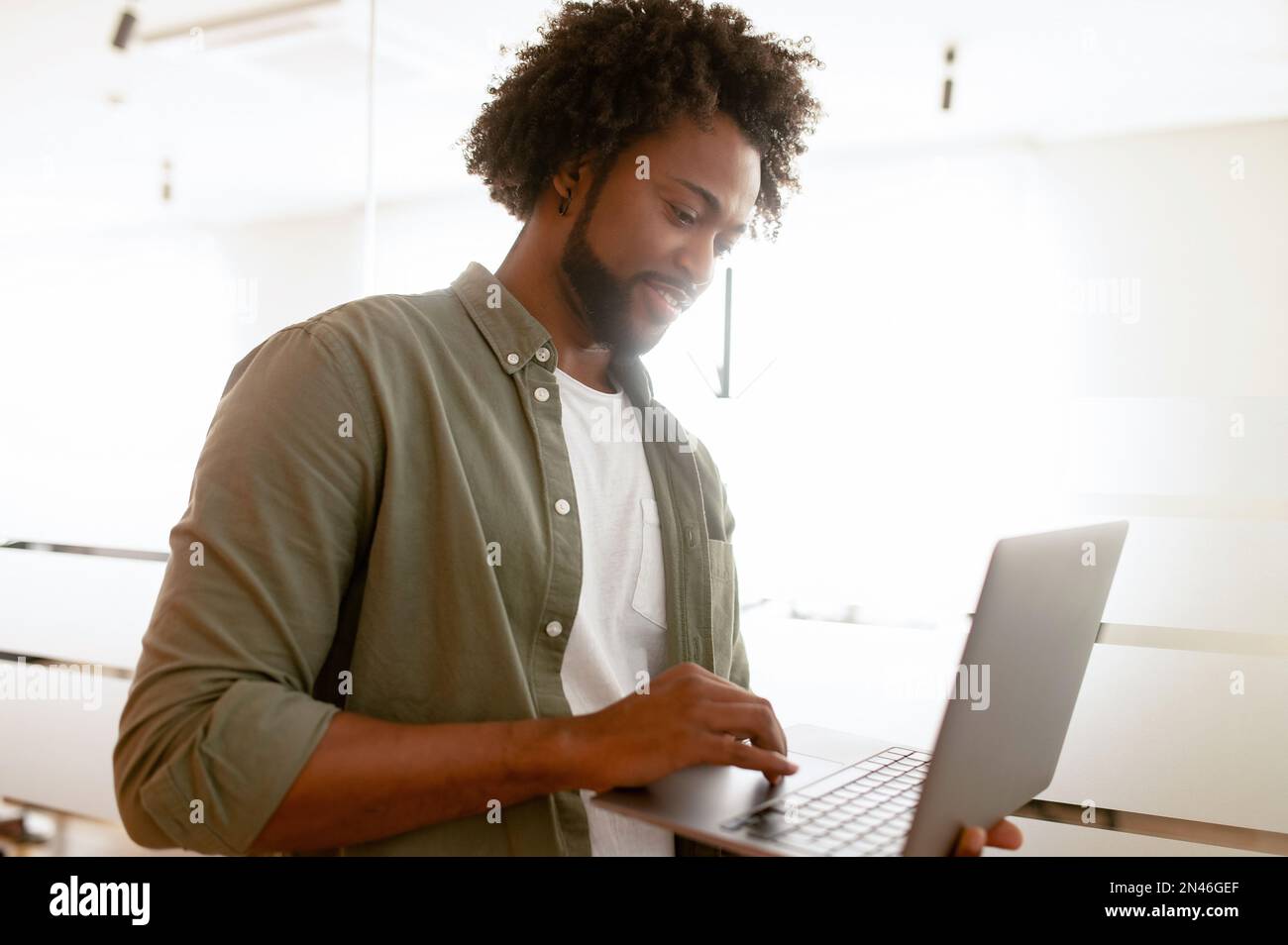 Optimistic african-american male office employee using laptop in modern ...