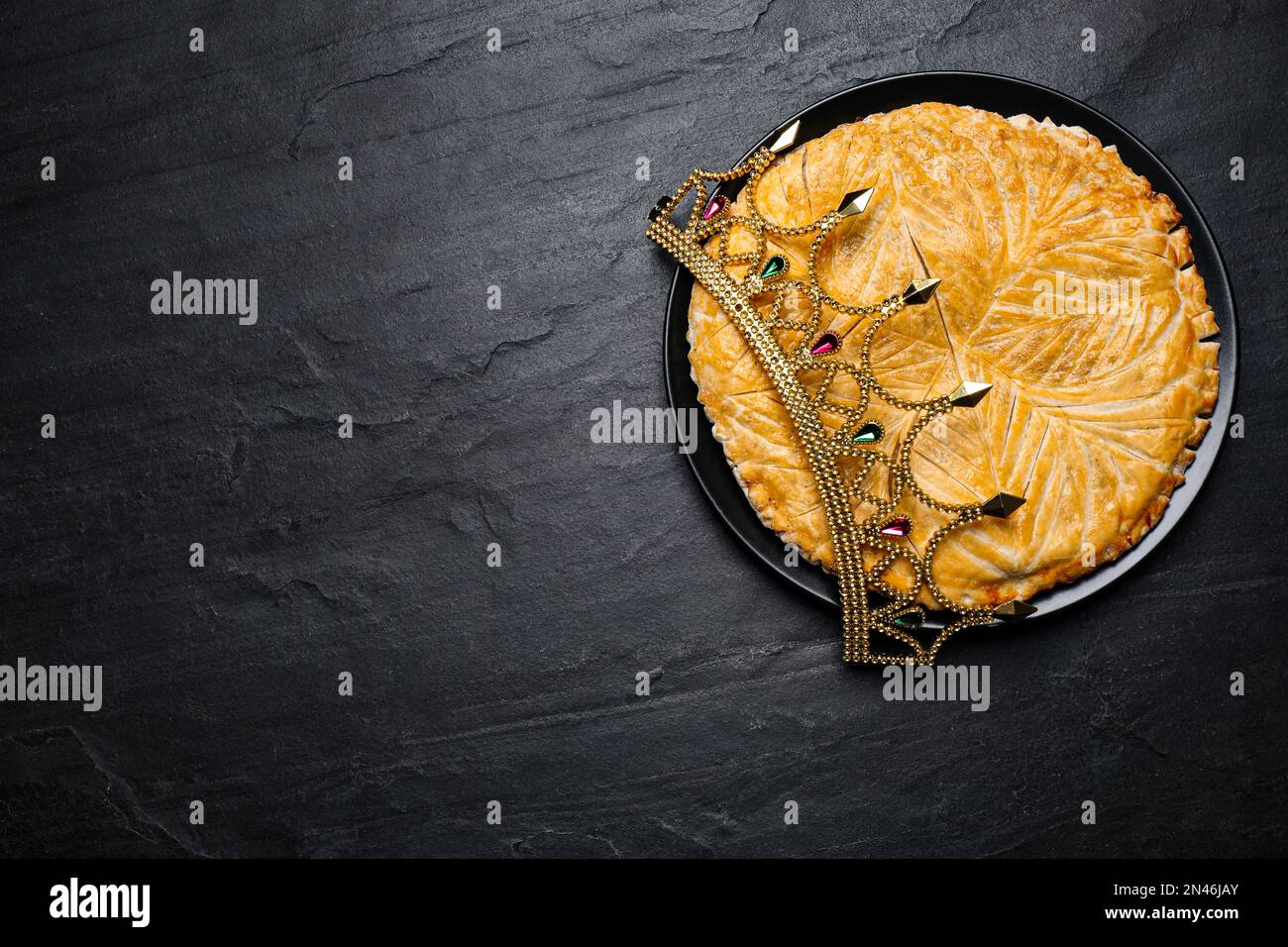 Traditional galette des rois with crown on black table, top view. Space ...