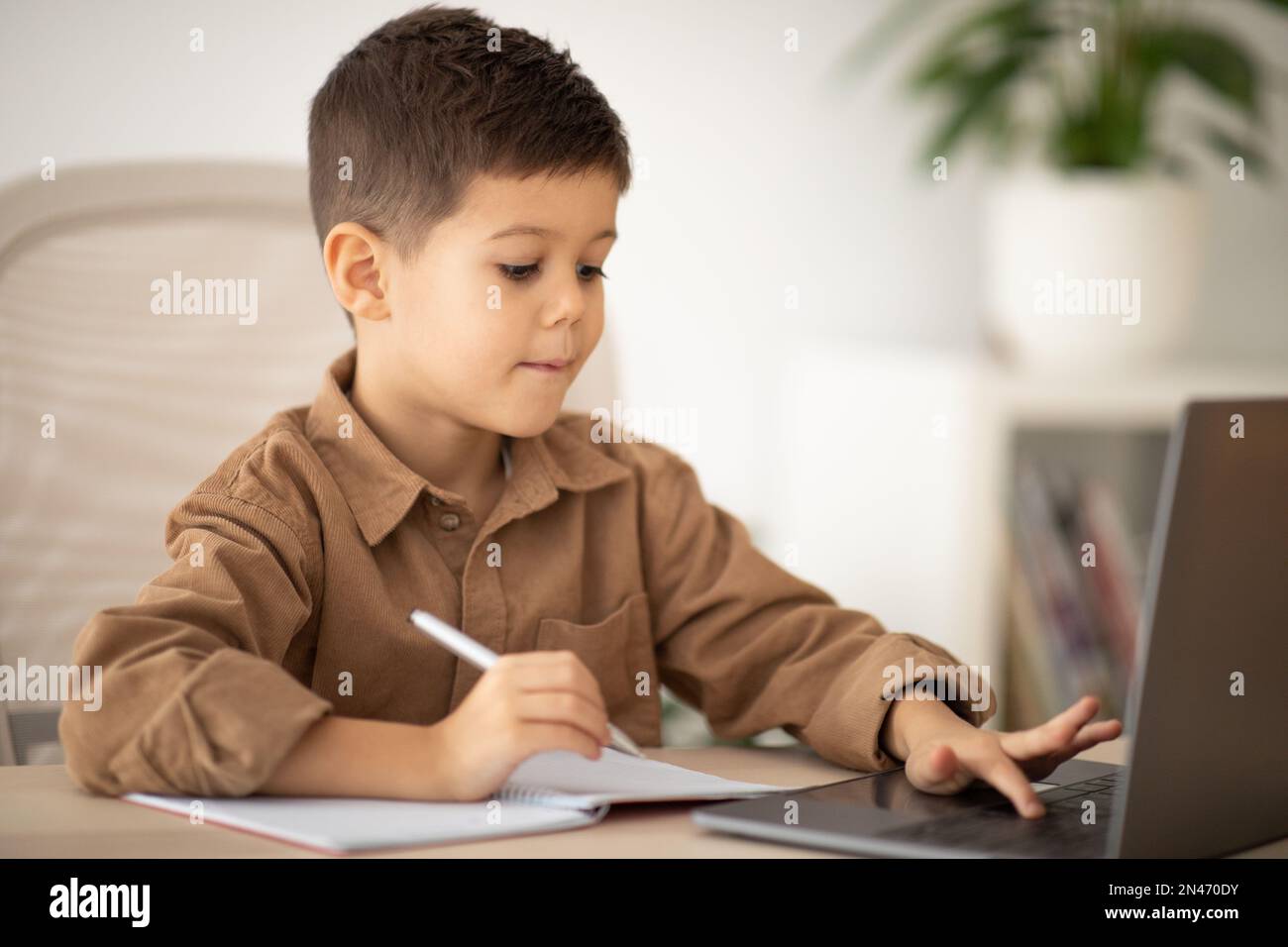 Busy caucasian little child sit at table making notes, watching lesson ...