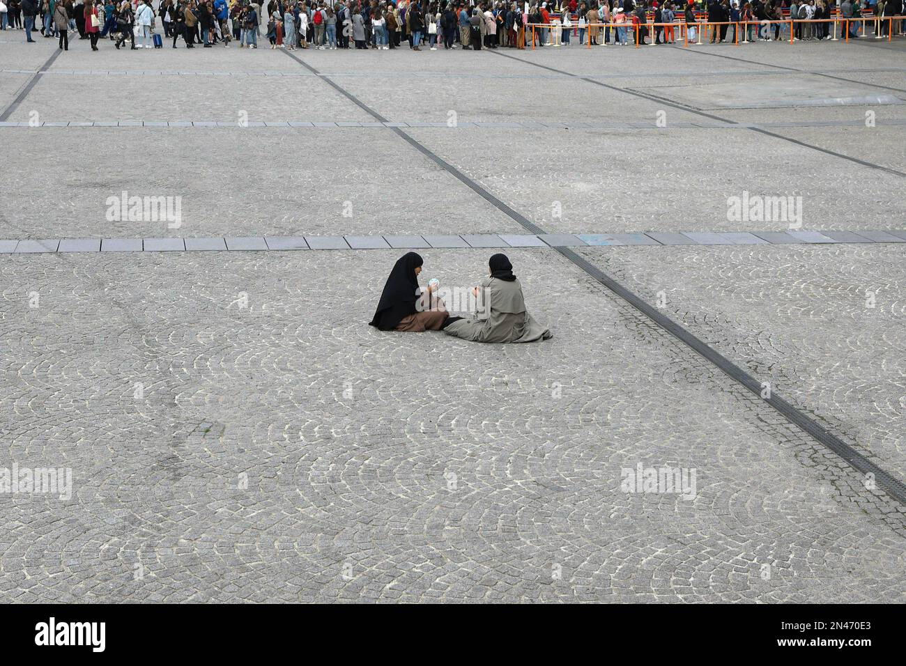 Two Muslim girls are sitting alone on the ground in a large asphalt ...