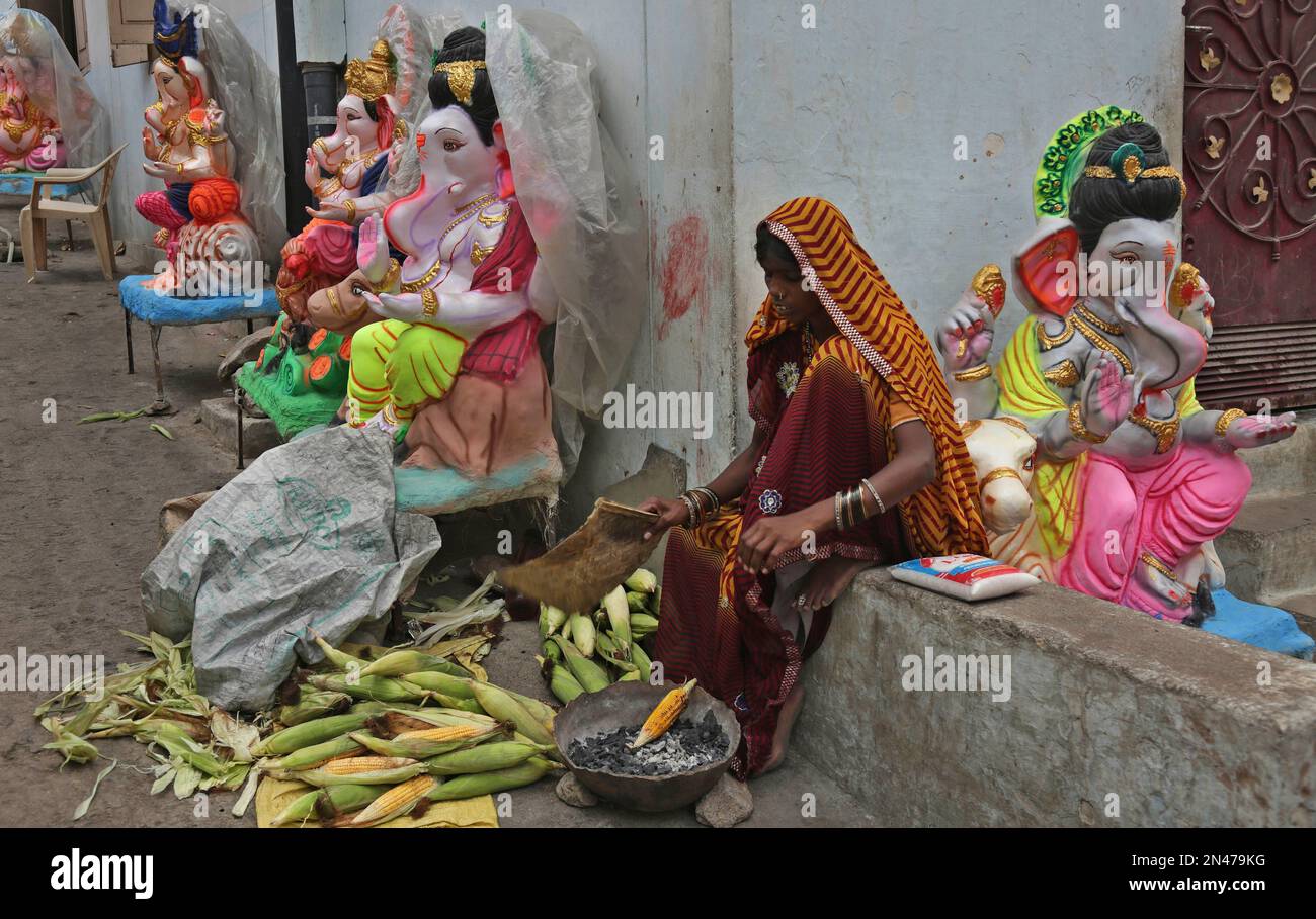 An Indian woman sells corn beside idols of elephant-headed Hindu God ...