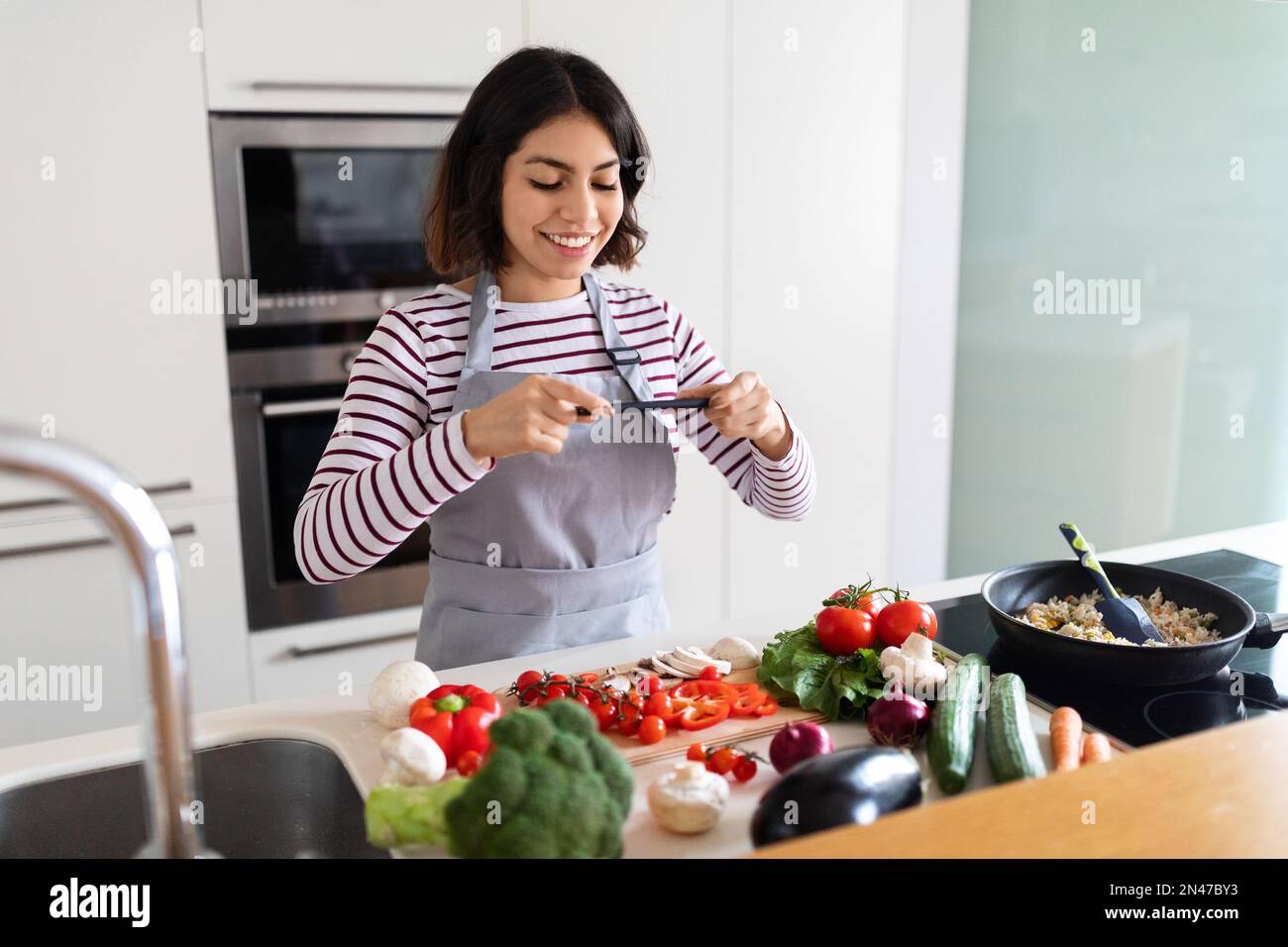 Young woman taking photo with phone while cooking in kitchen Stock ...