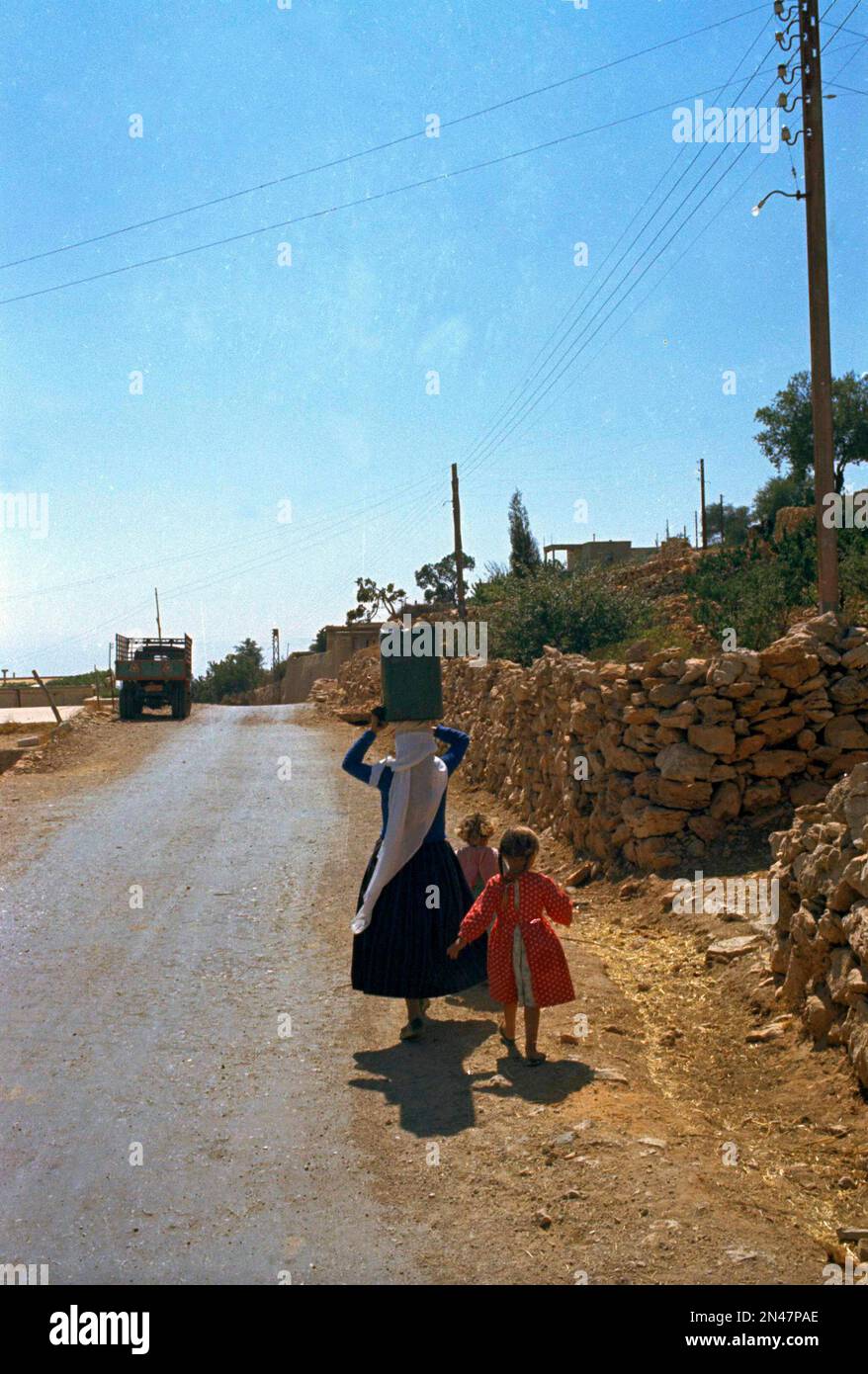 A woman carrying wares atop her head and two children walk along a ...